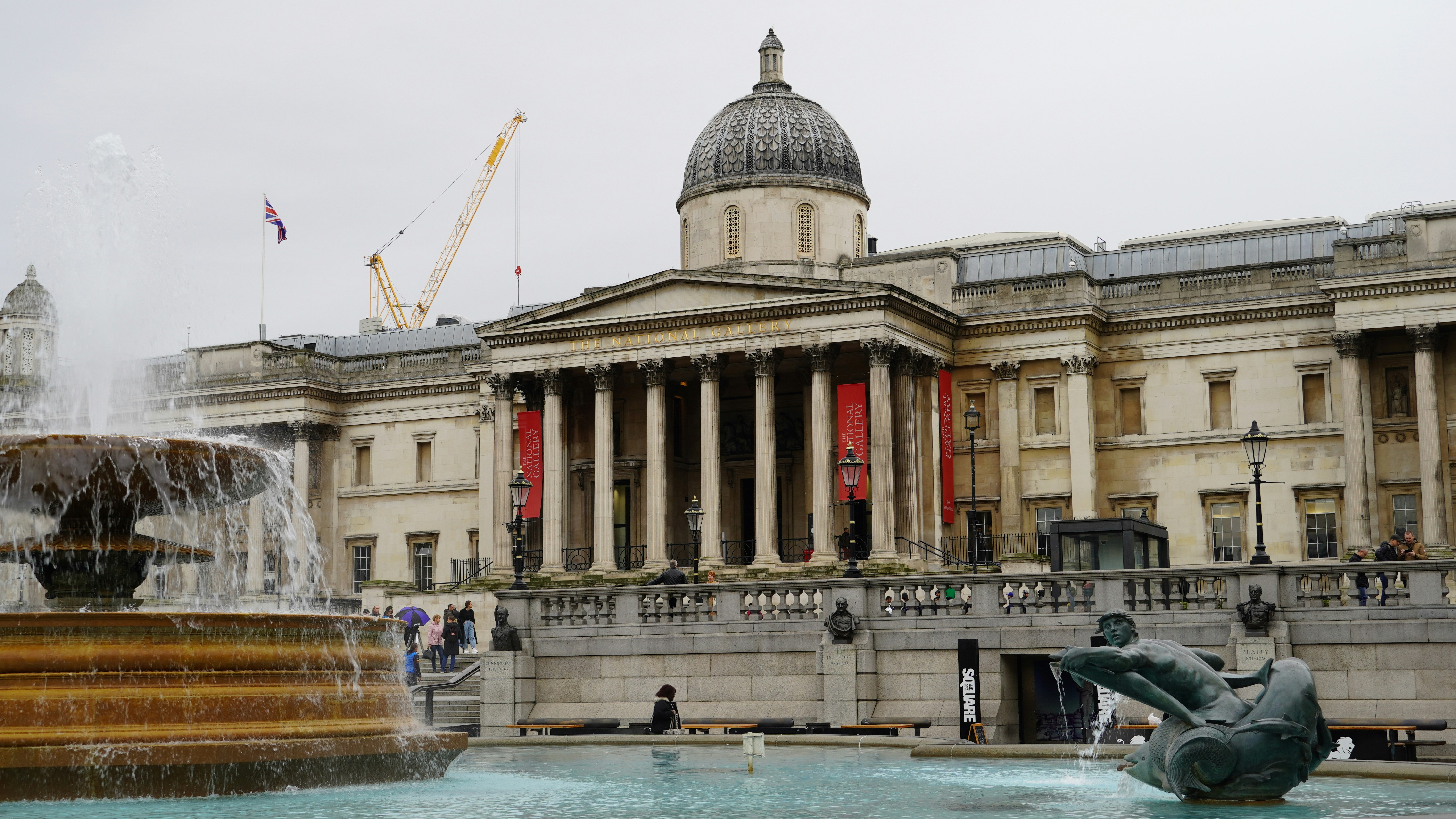 Historic architecture of the National Gallery framed by a vibrant fountain and sculpture in Trafalgar Square.