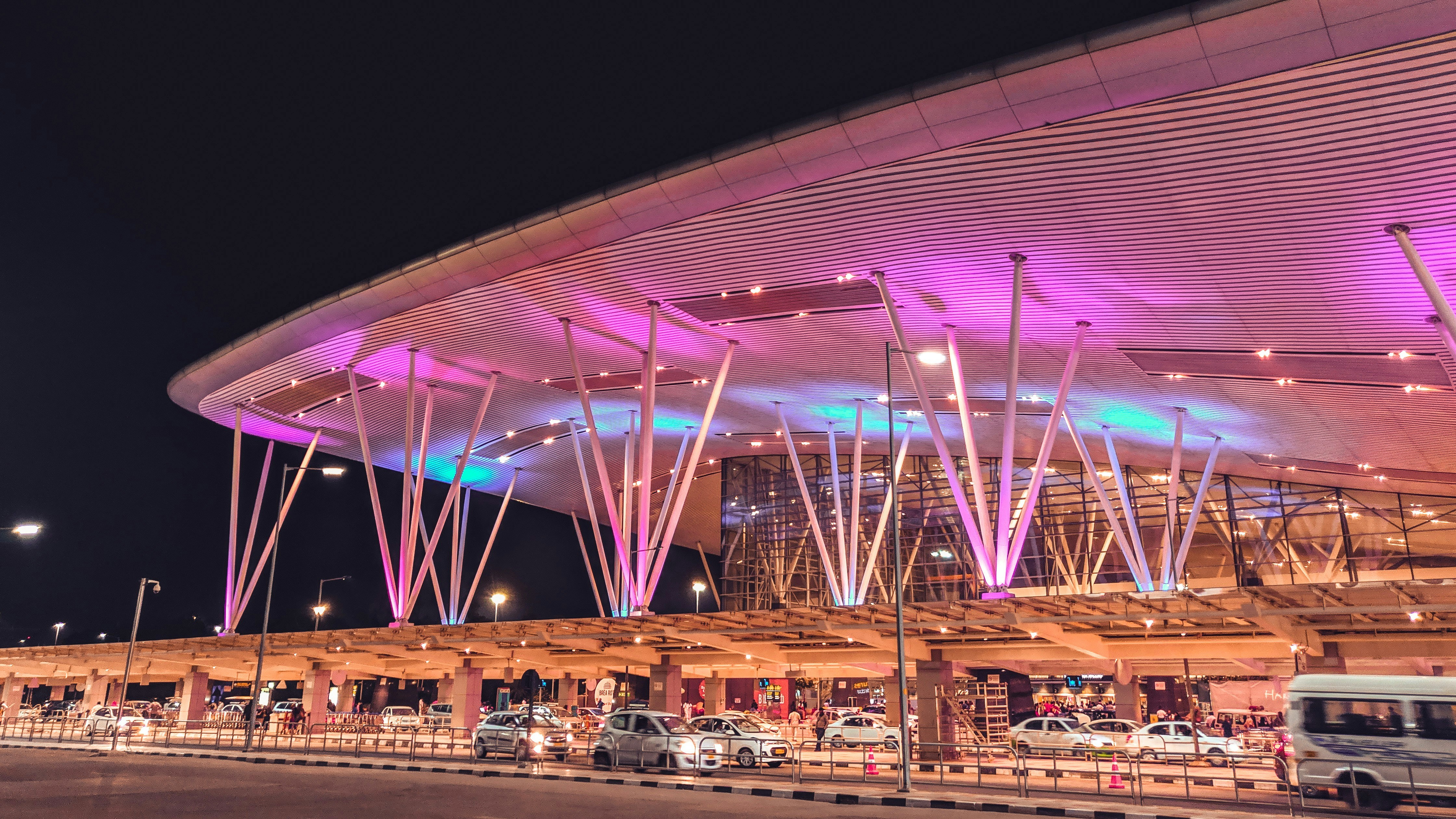 Vibrant airport terminal illuminated by colorful lights, showcasing contemporary architectural design. The structure's sleek lines and dynamic supports create an inviting atmosphere.