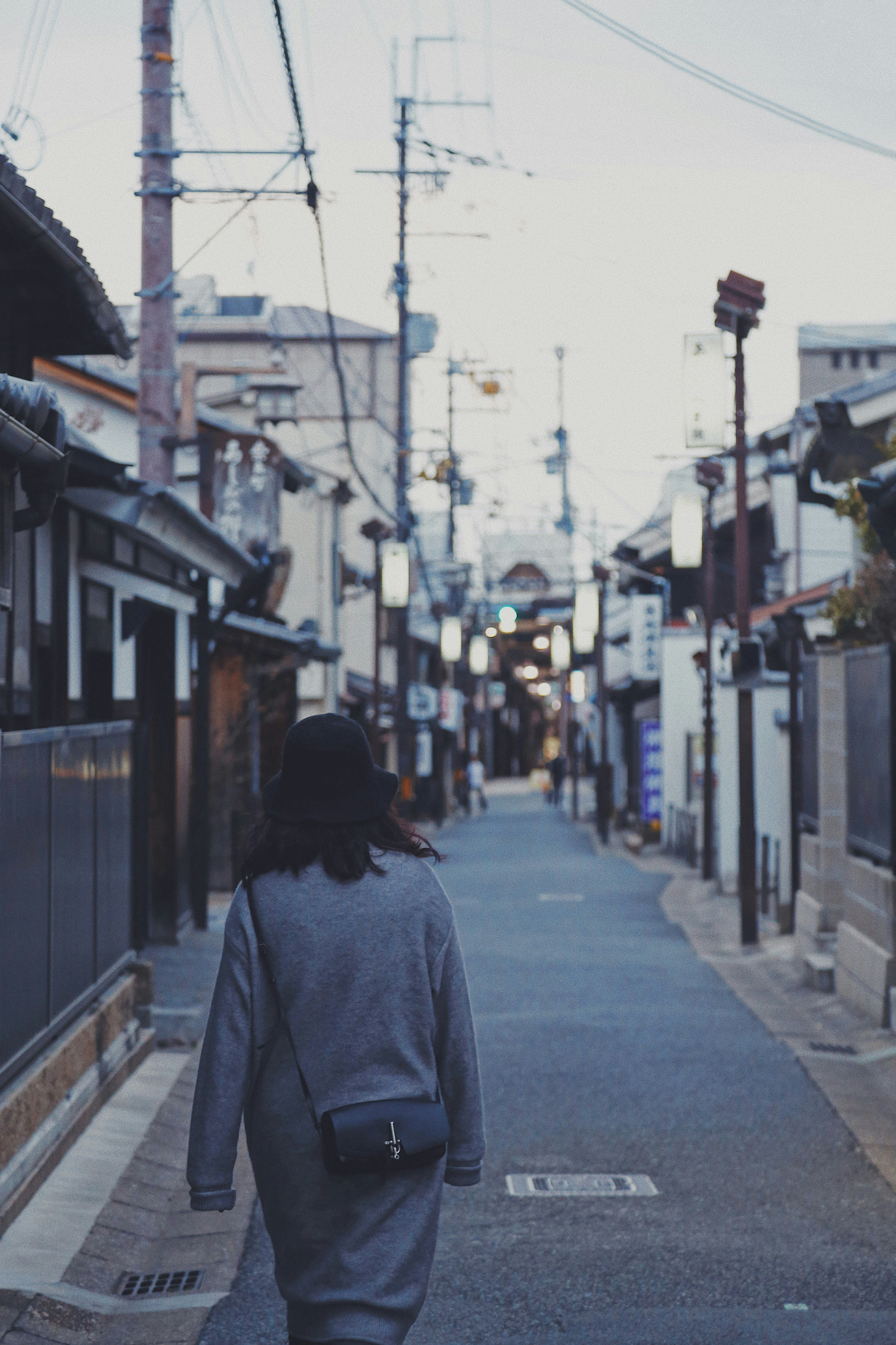 A solitary figure walks down a narrow, dimly lit street lined with traditional buildings and lanterns, evoking a sense of nostalgia and tranquility.