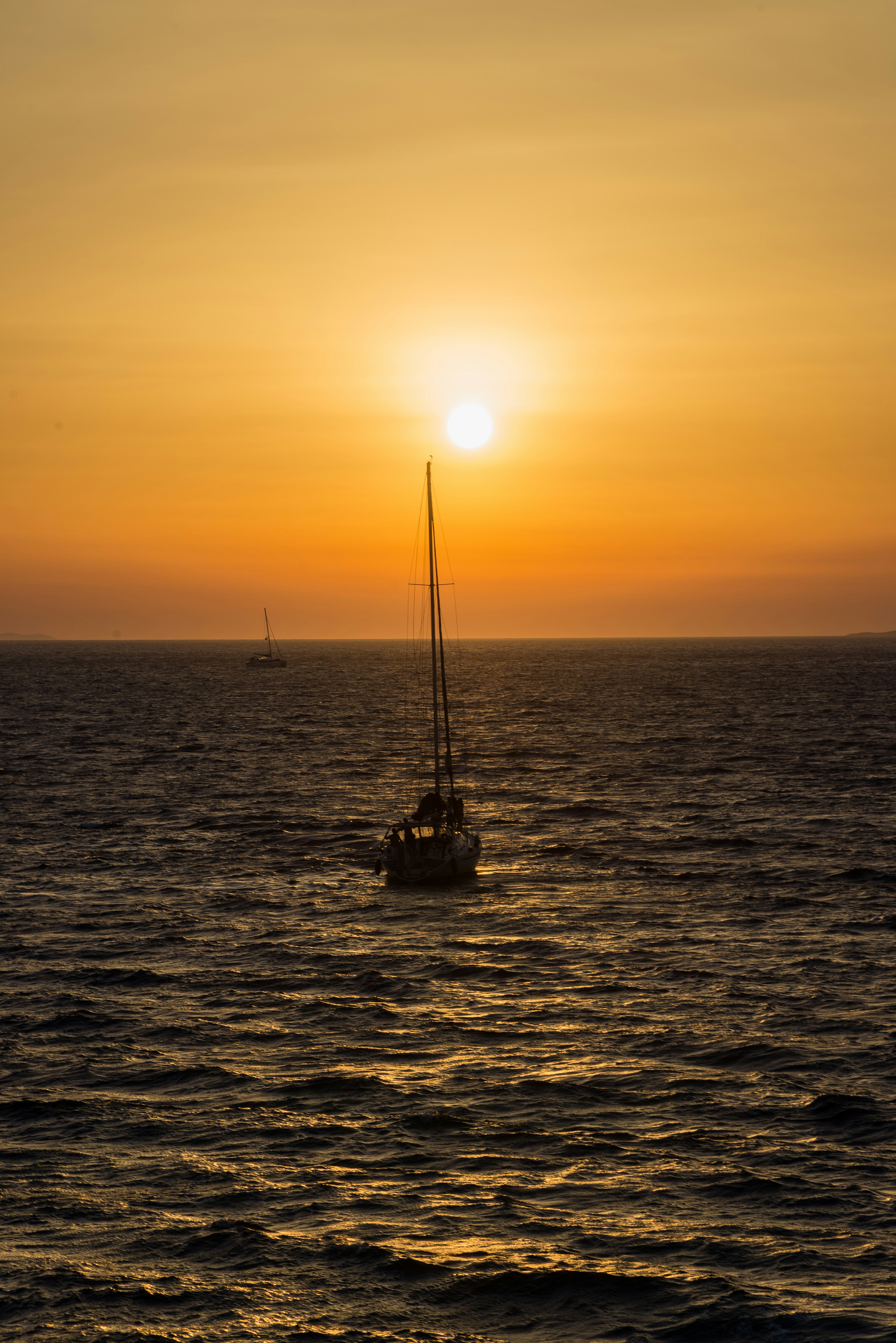 A solitary sailboat glides across shimmering waters as the sun sets, casting a warm golden glow over the scene.