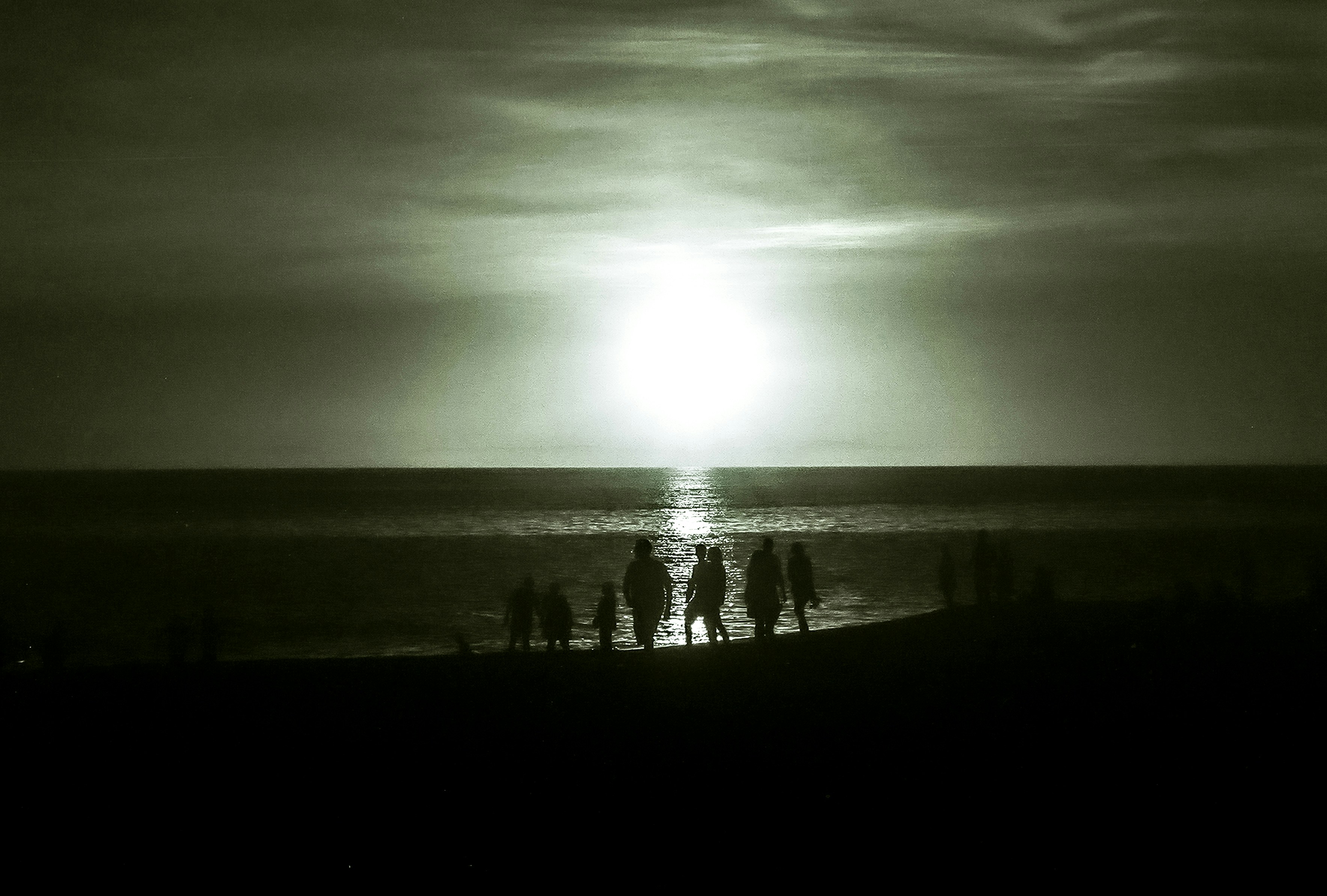 Silhouetted figures walking along a beach at sunset, with the sun reflecting on the water's surface.