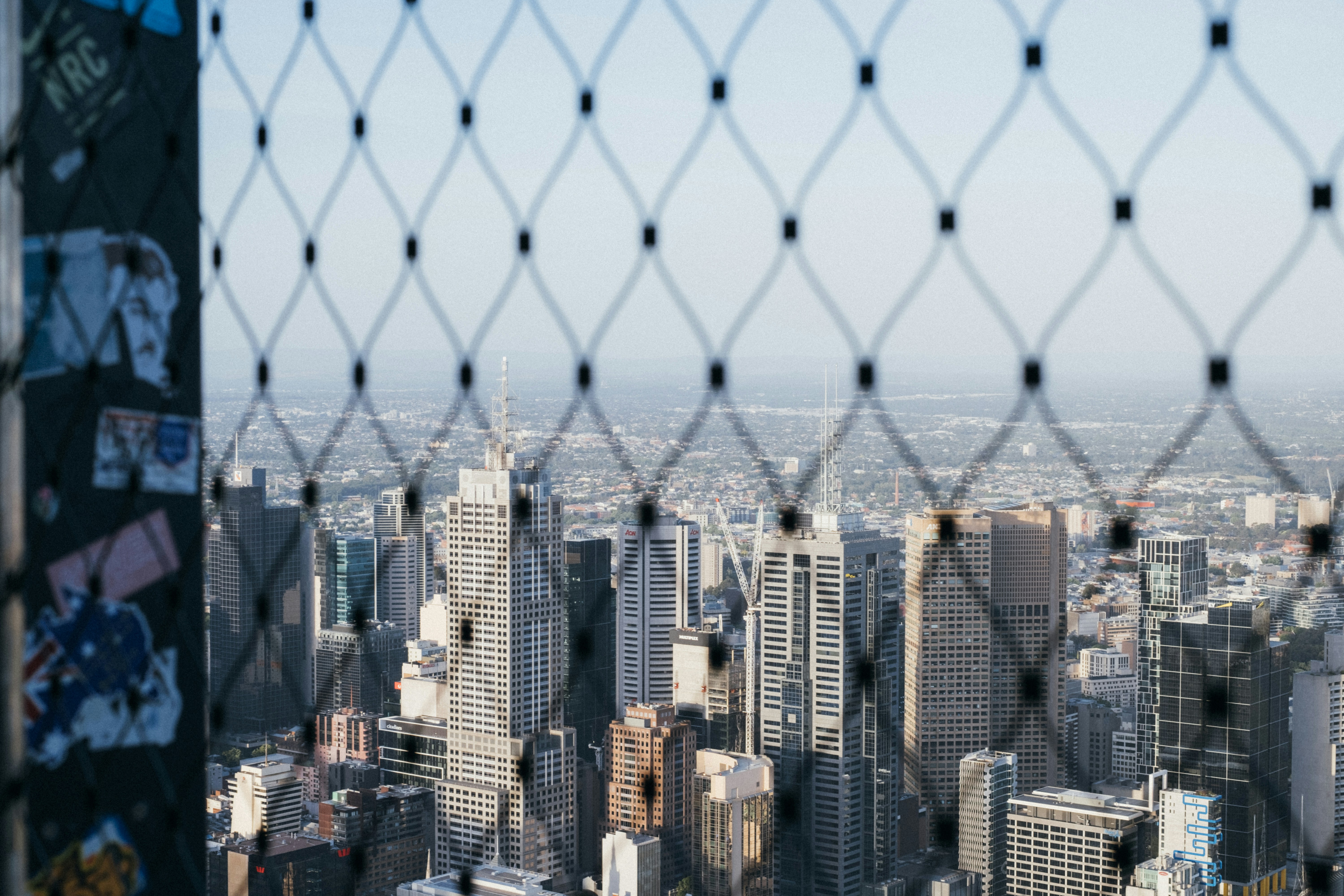 City skyline framed by a metal mesh fence under a clear sky.