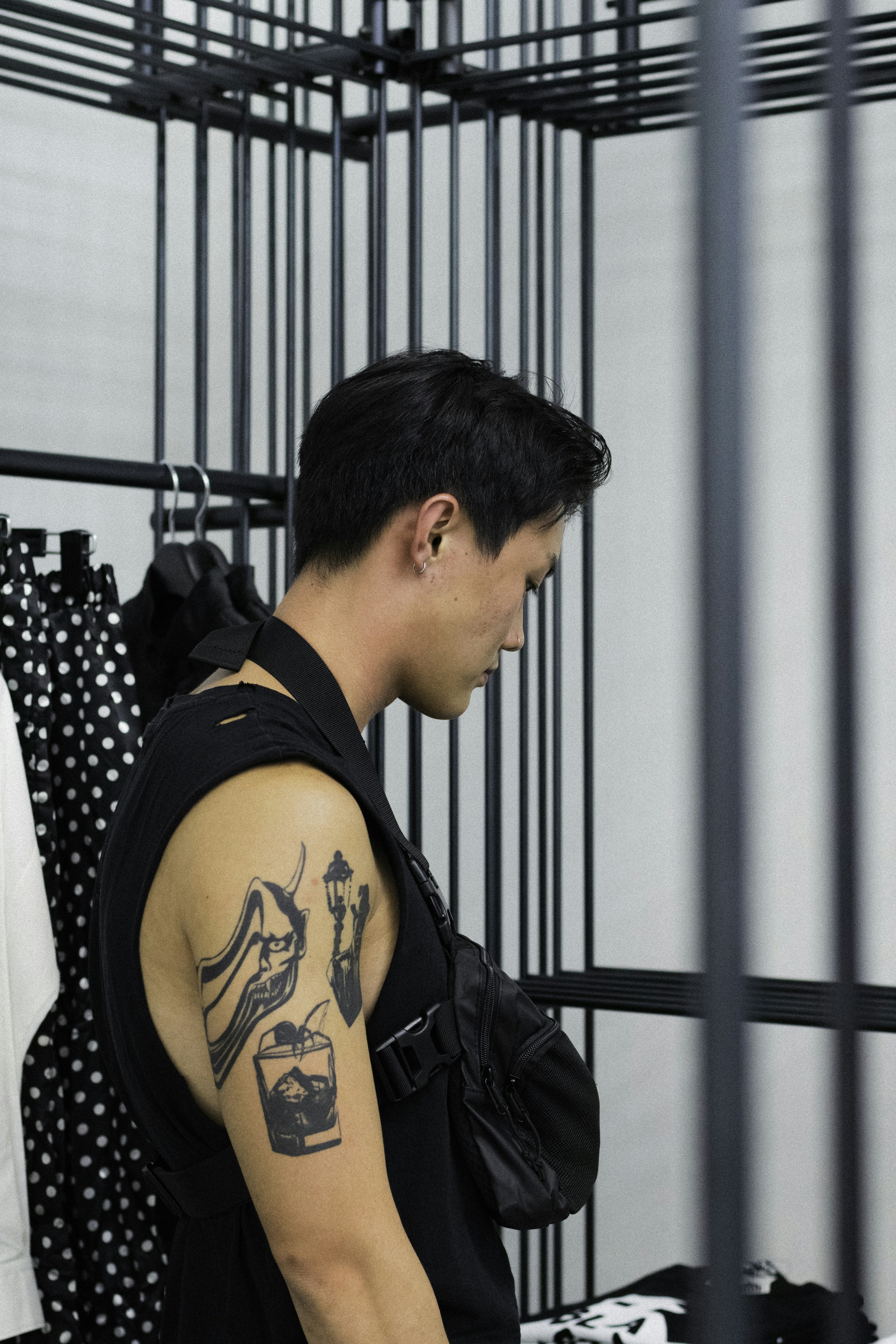 A young man with a striking tattoo examines clothing in a minimalist retail space, showcasing a blend of fashion and individuality.