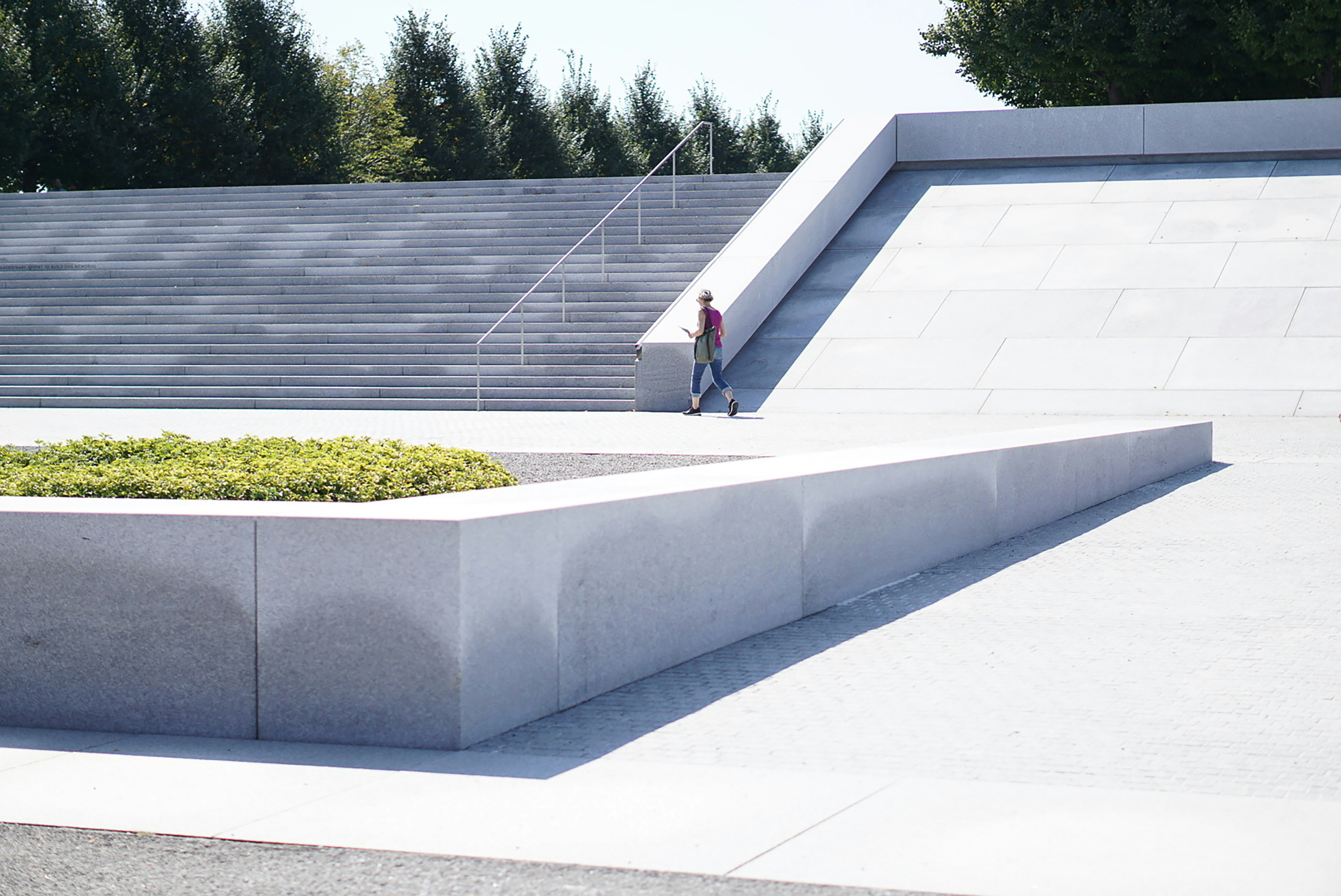 Person walking on minimalist concrete structure surrounded by greenery and trees.