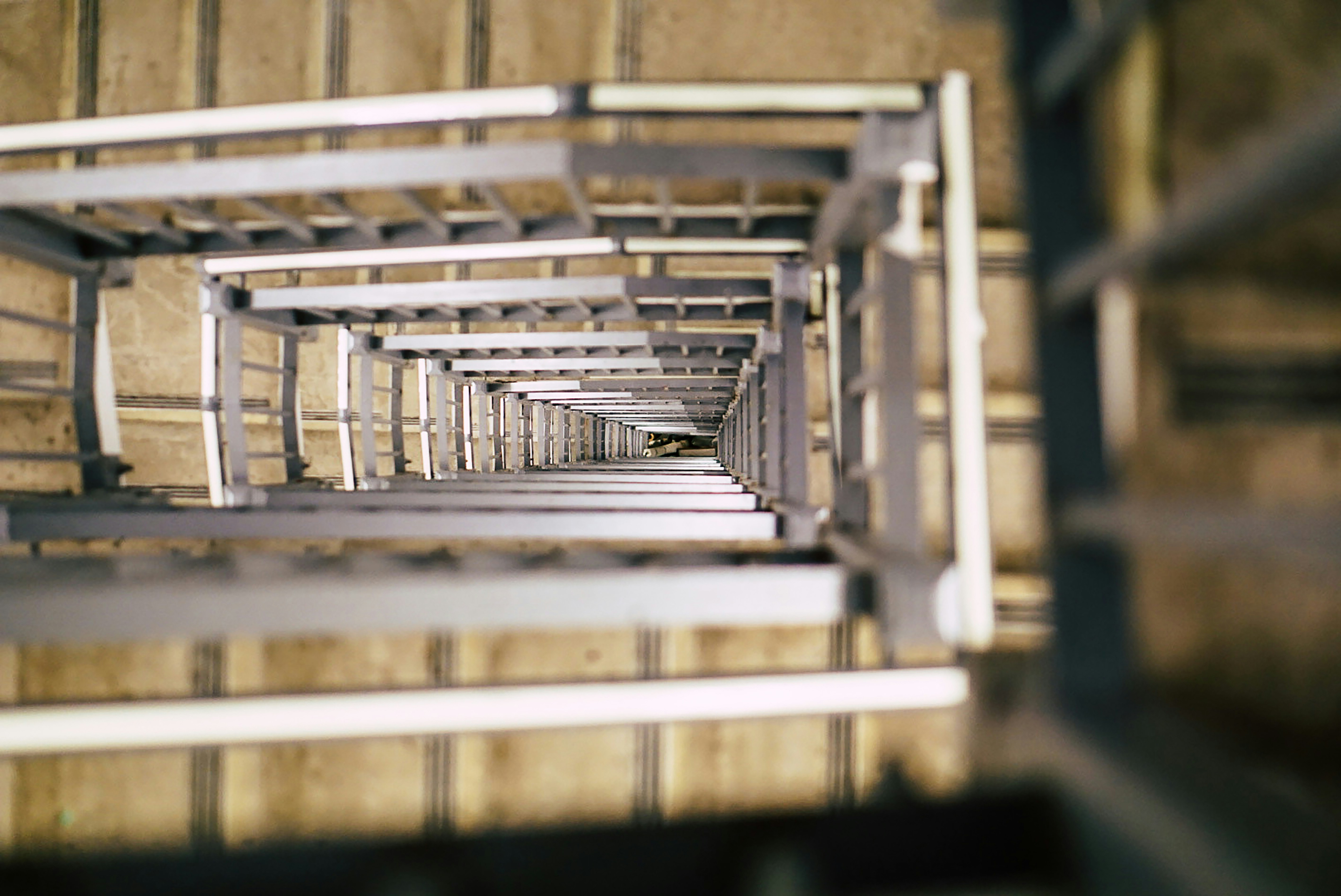 Aerial view looking down a metallic ladder, showcasing its geometric patterns against a textured surface.