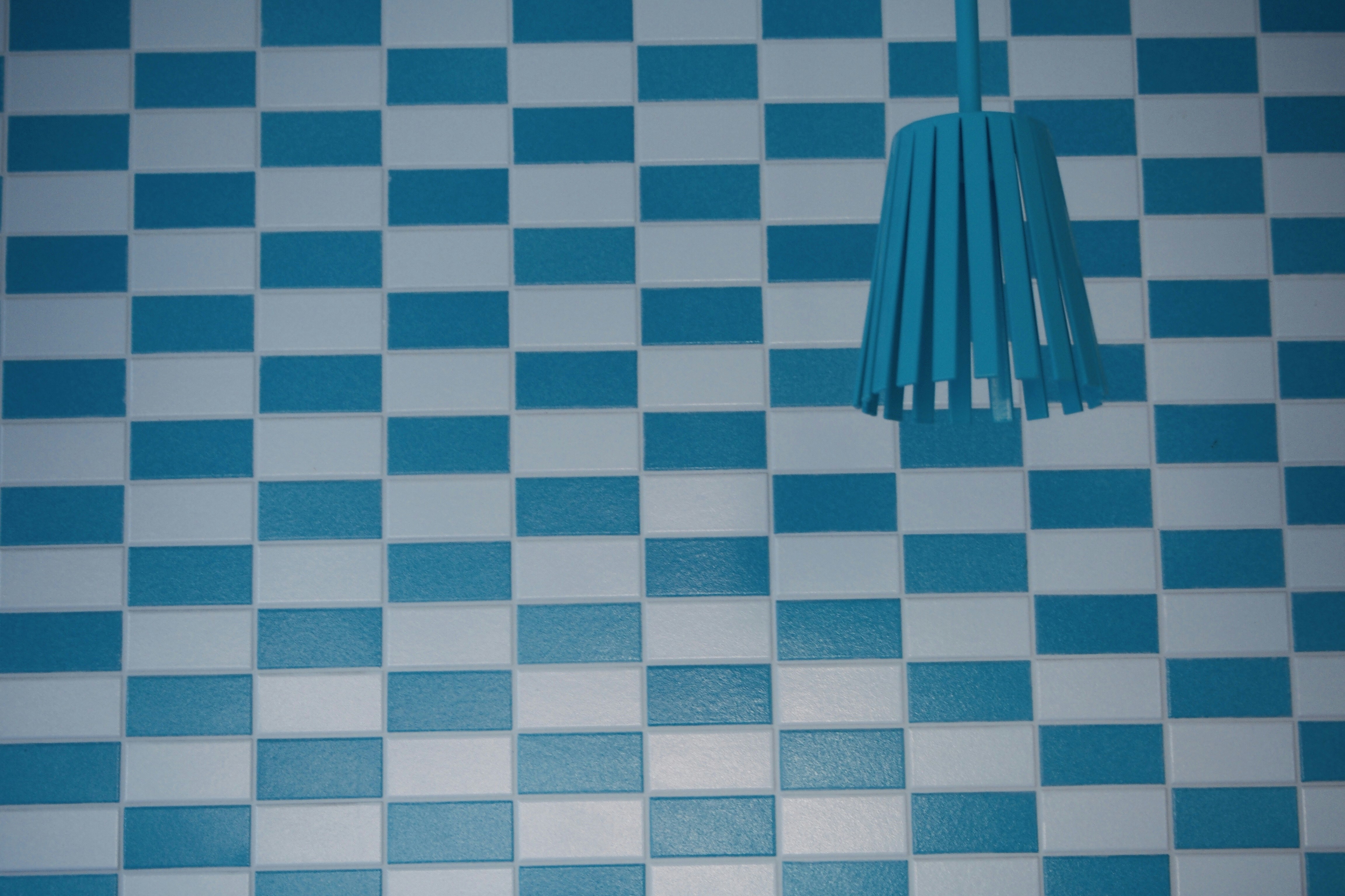 A playful blue pendant light hangs against a checkered turquoise and white background, emphasizing geometric patterns and color contrast.