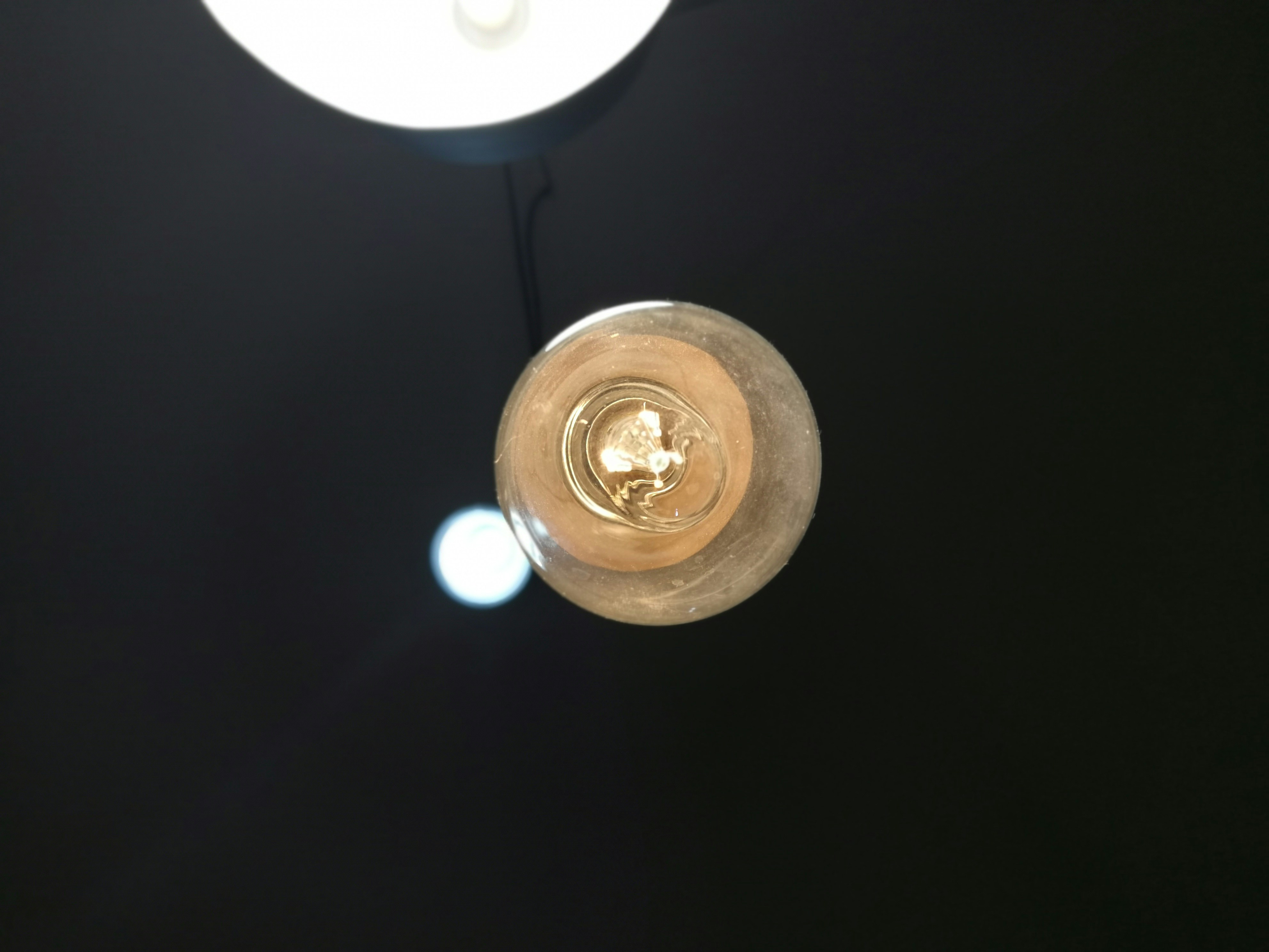 Close-up view of a light bulb suspended from the ceiling, showcasing its intricate filament against a dark backdrop.