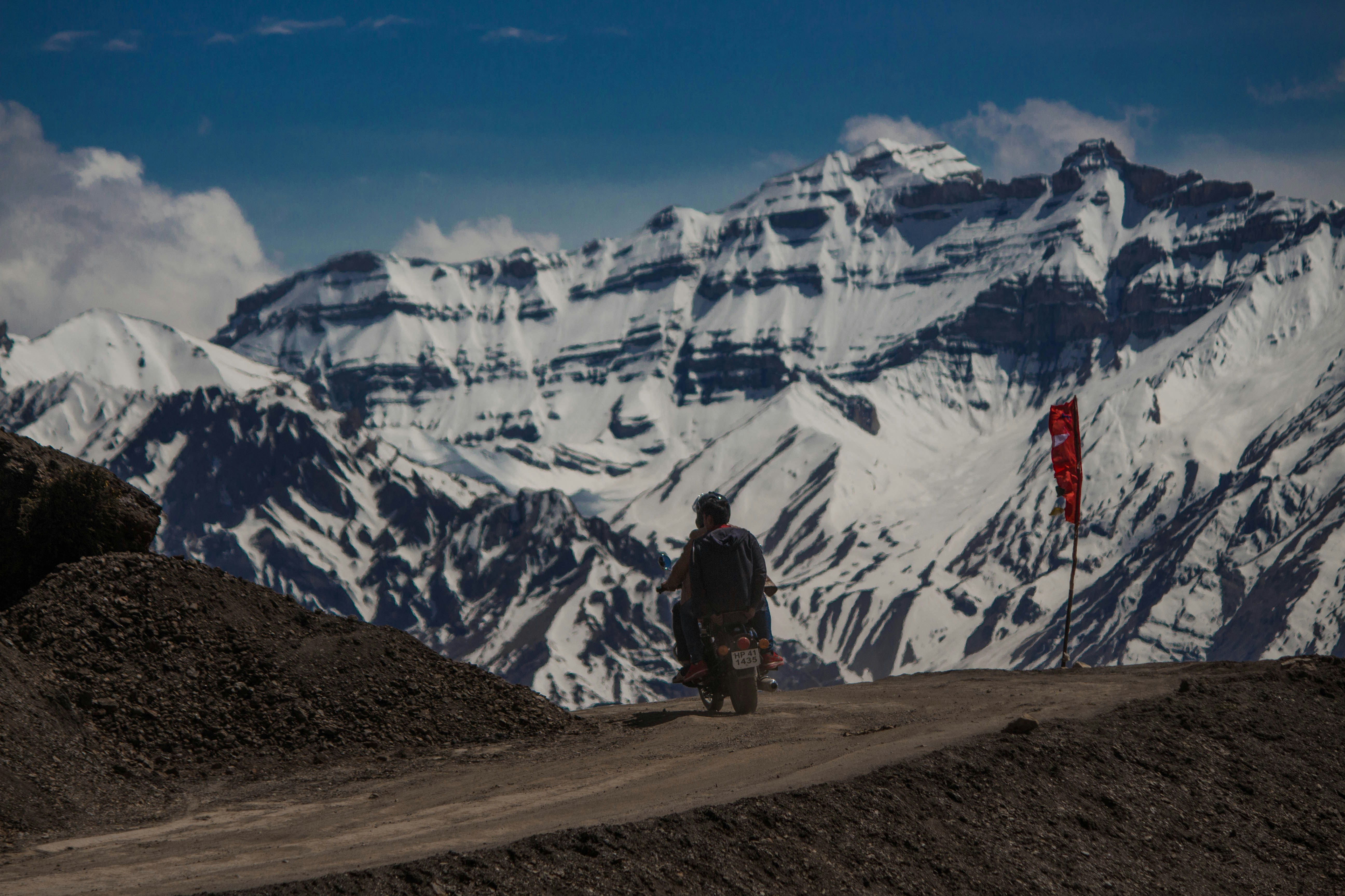 Motorcyclist navigating a rugged path with towering snow-covered mountains in the background.