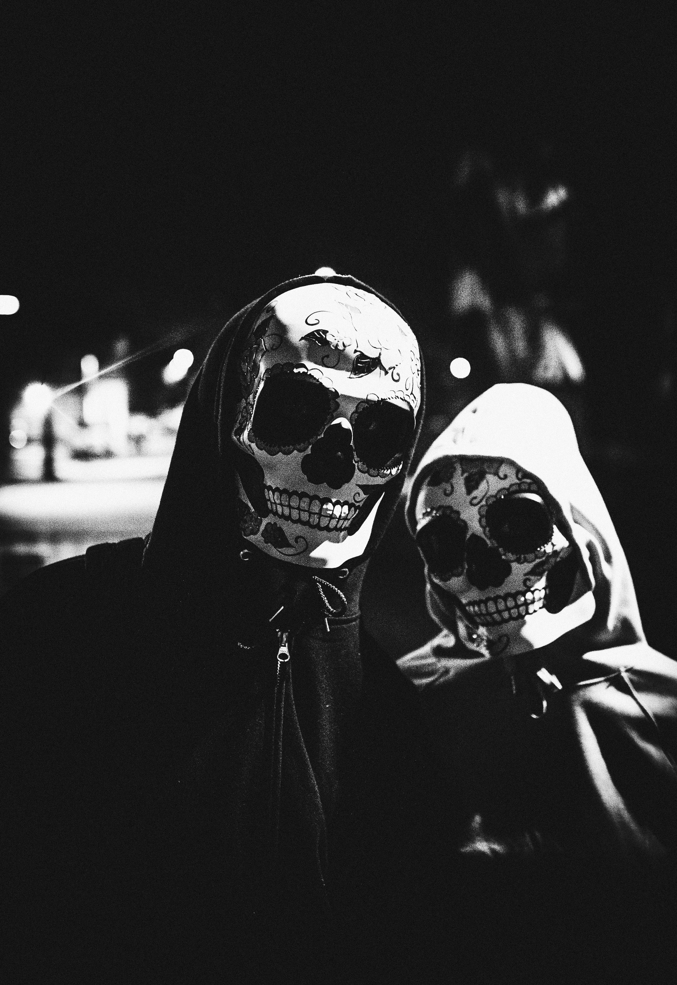 Two figures in skeleton masks pose under dim streetlights, exuding an eerie Halloween ambiance.