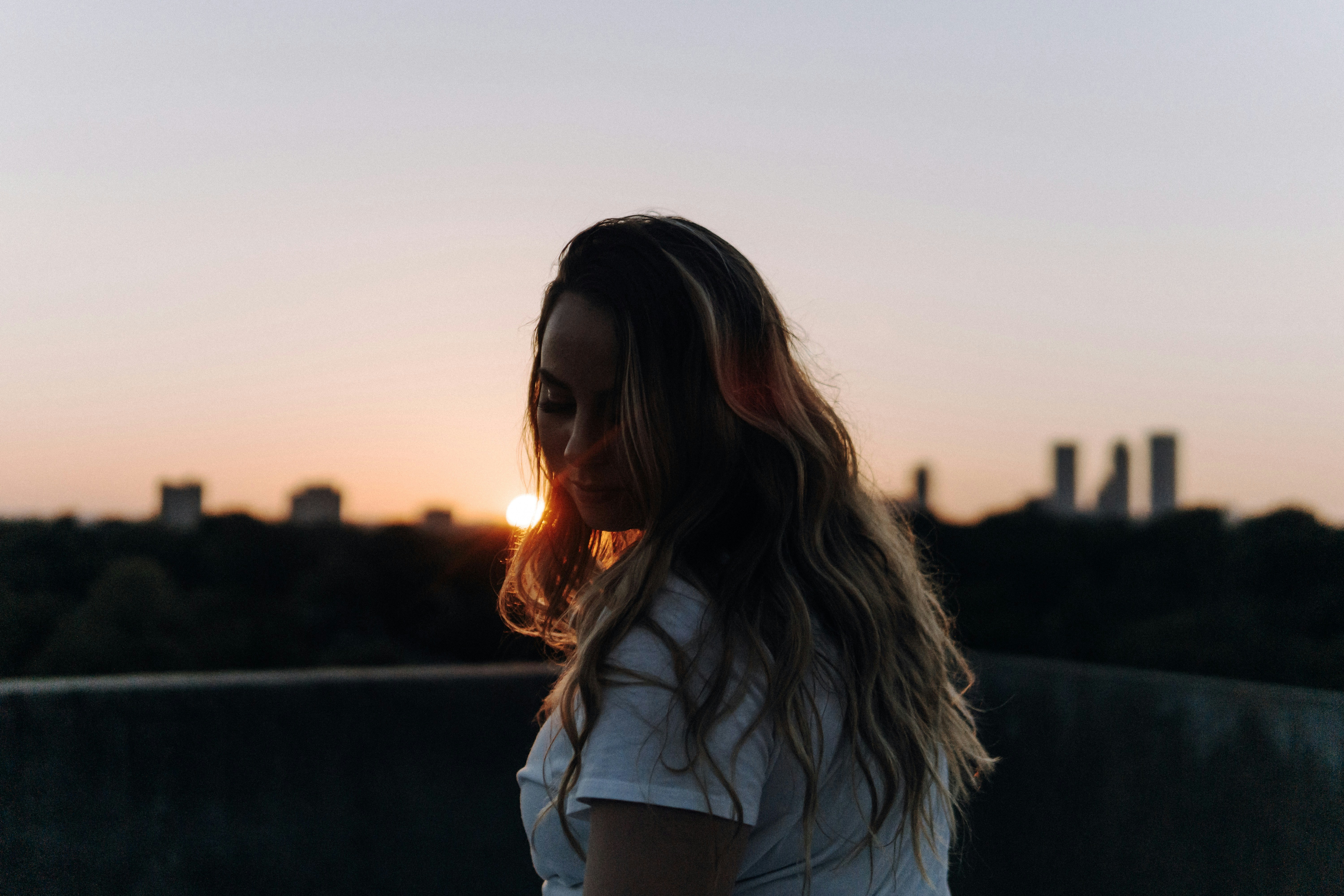 Person in a white t-shirt glancing sideways, silhouetted against a vibrant sunset backdrop.