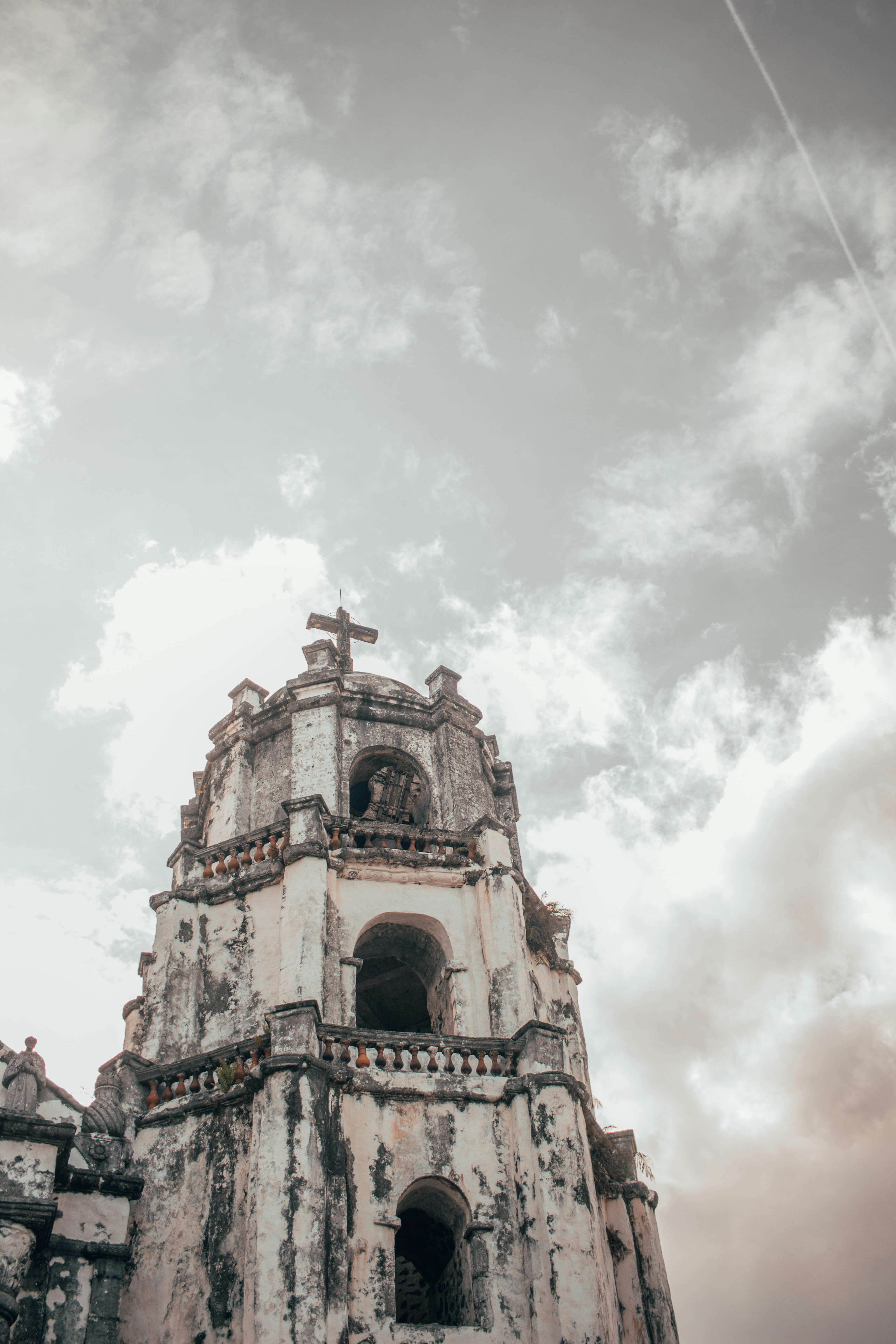 A weathered church tower rises against a cloudy sky, showcasing intricate architectural details and a prominent cross atop. The scene evokes a sense of history and spirituality.