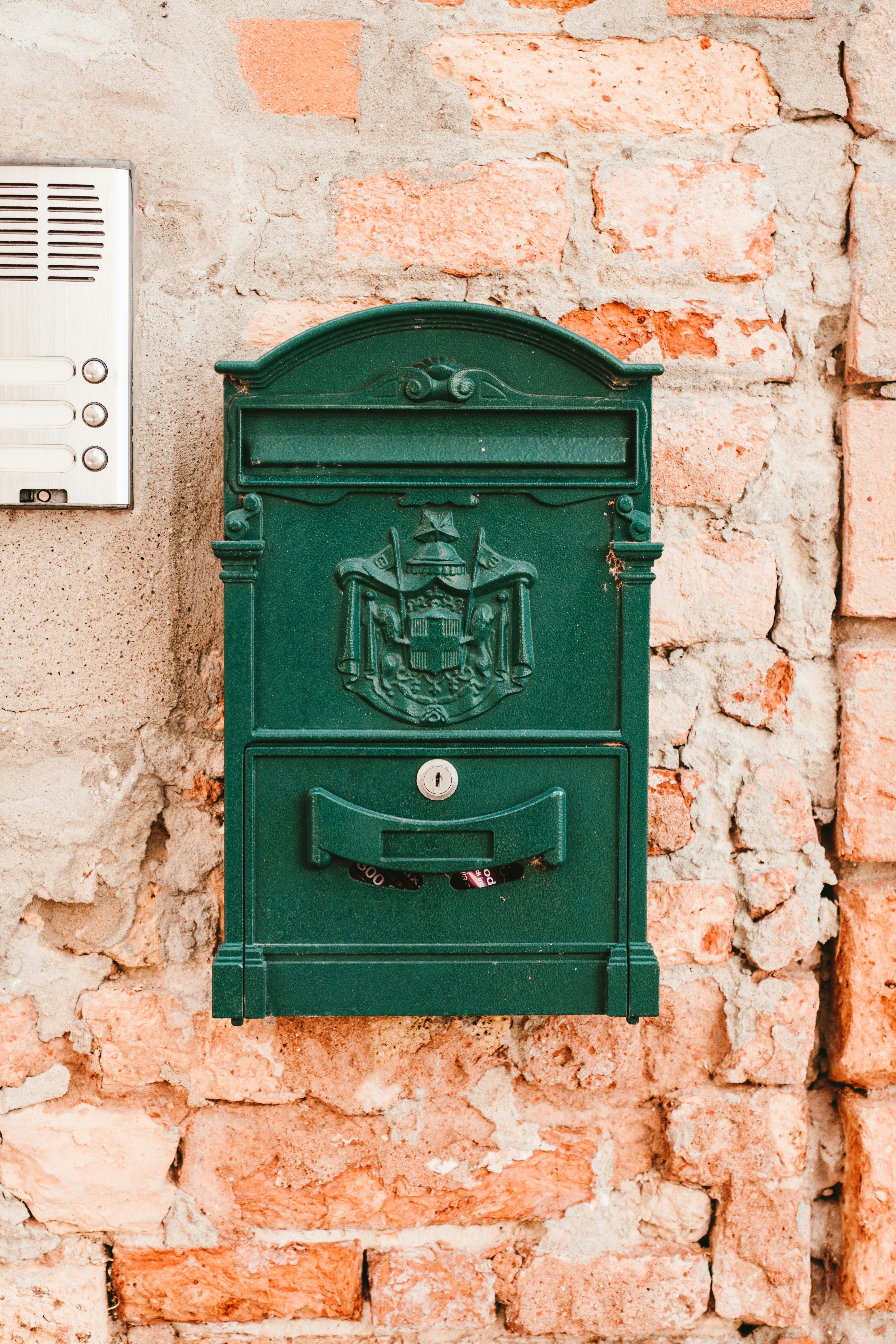 A vintage green mailbox adorned with a crest, mounted on a weathered brick wall showcasing a blend of textures and colors.