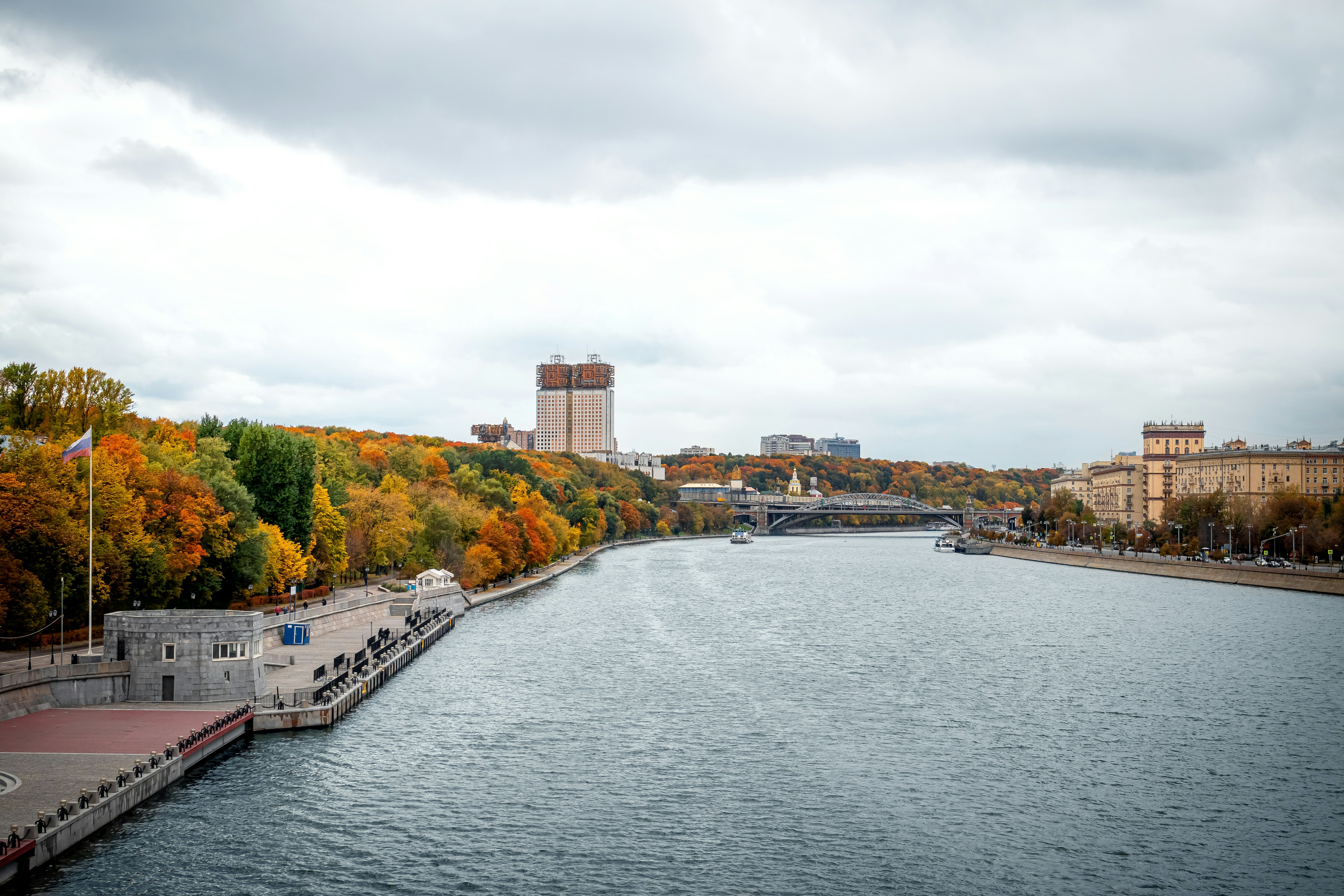 Autumn Riverfront: A Quiet Cityscape Framed by Russet Trees and a Distant Bridge