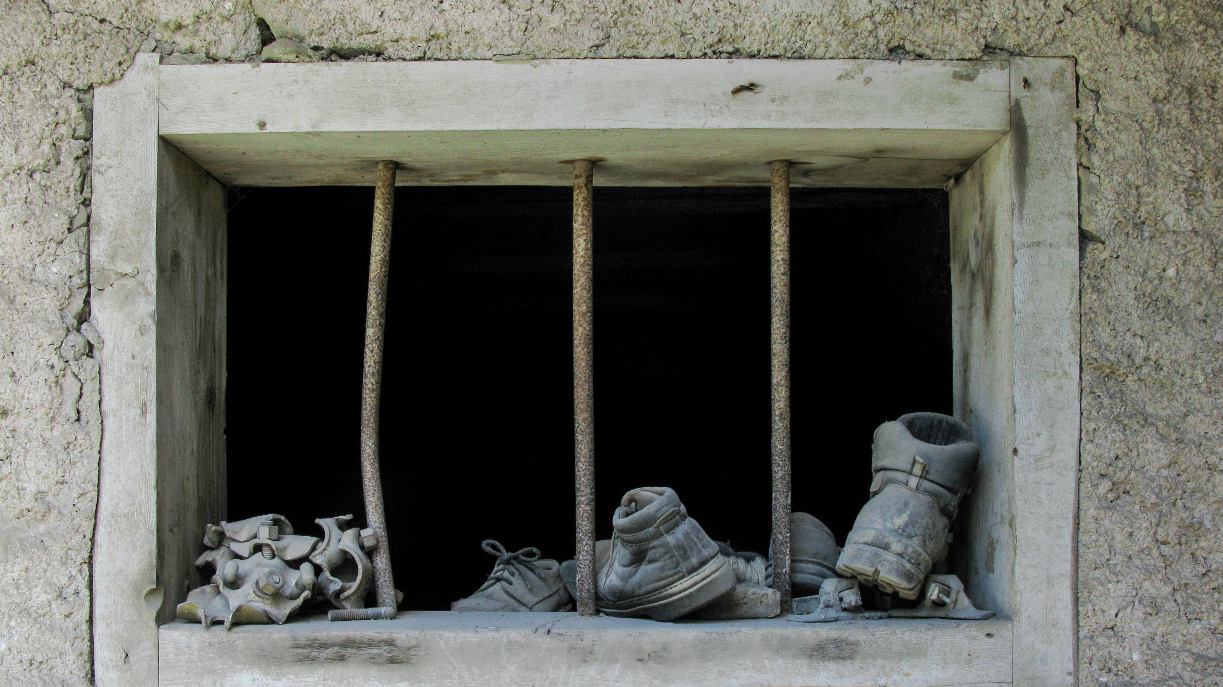 Abandoned window with rusted bars and scattered shoes on the sill, set against a dark interior.