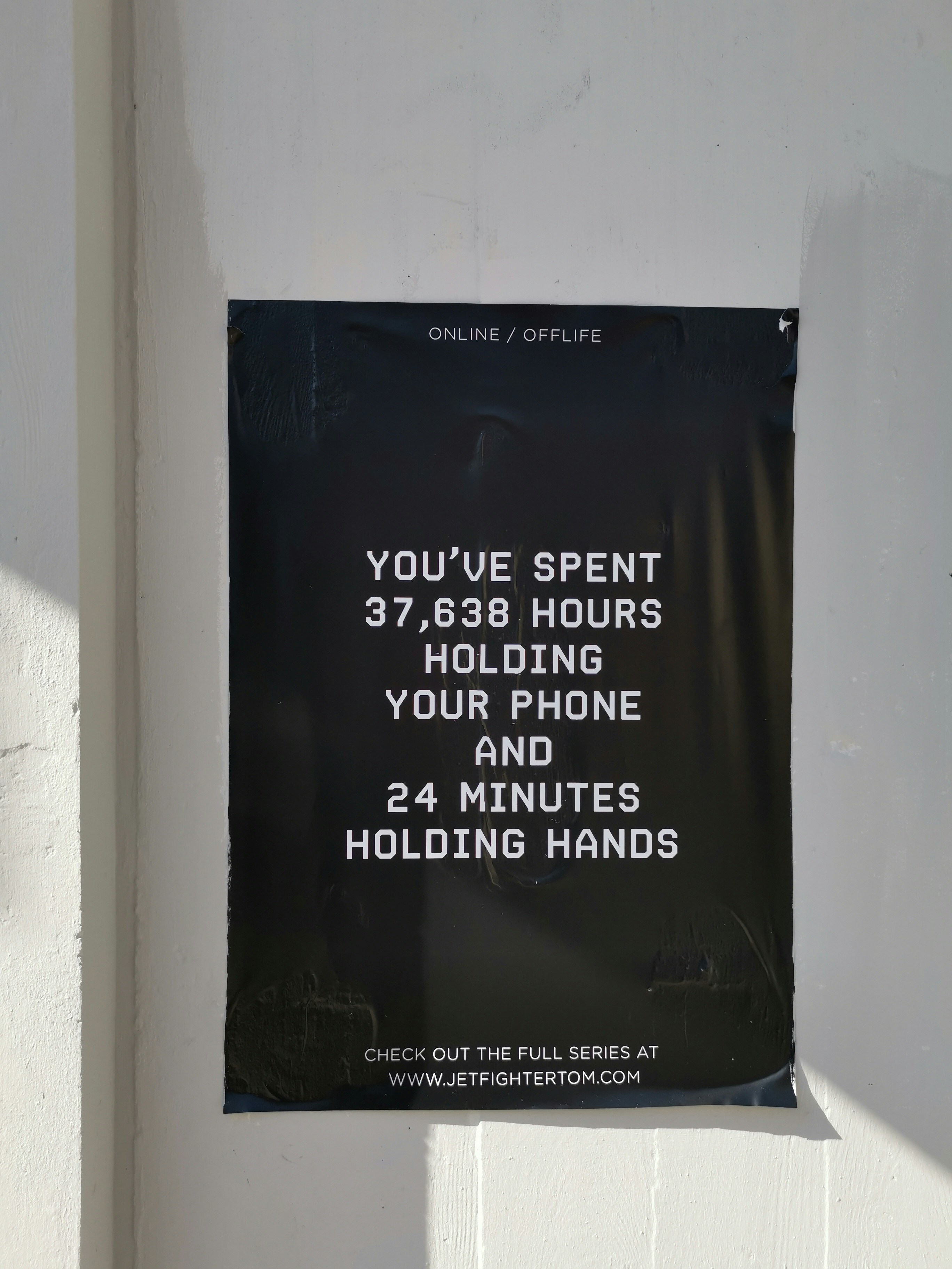 Bold text on a black poster highlighting the contrast between time spent on devices and human interaction.