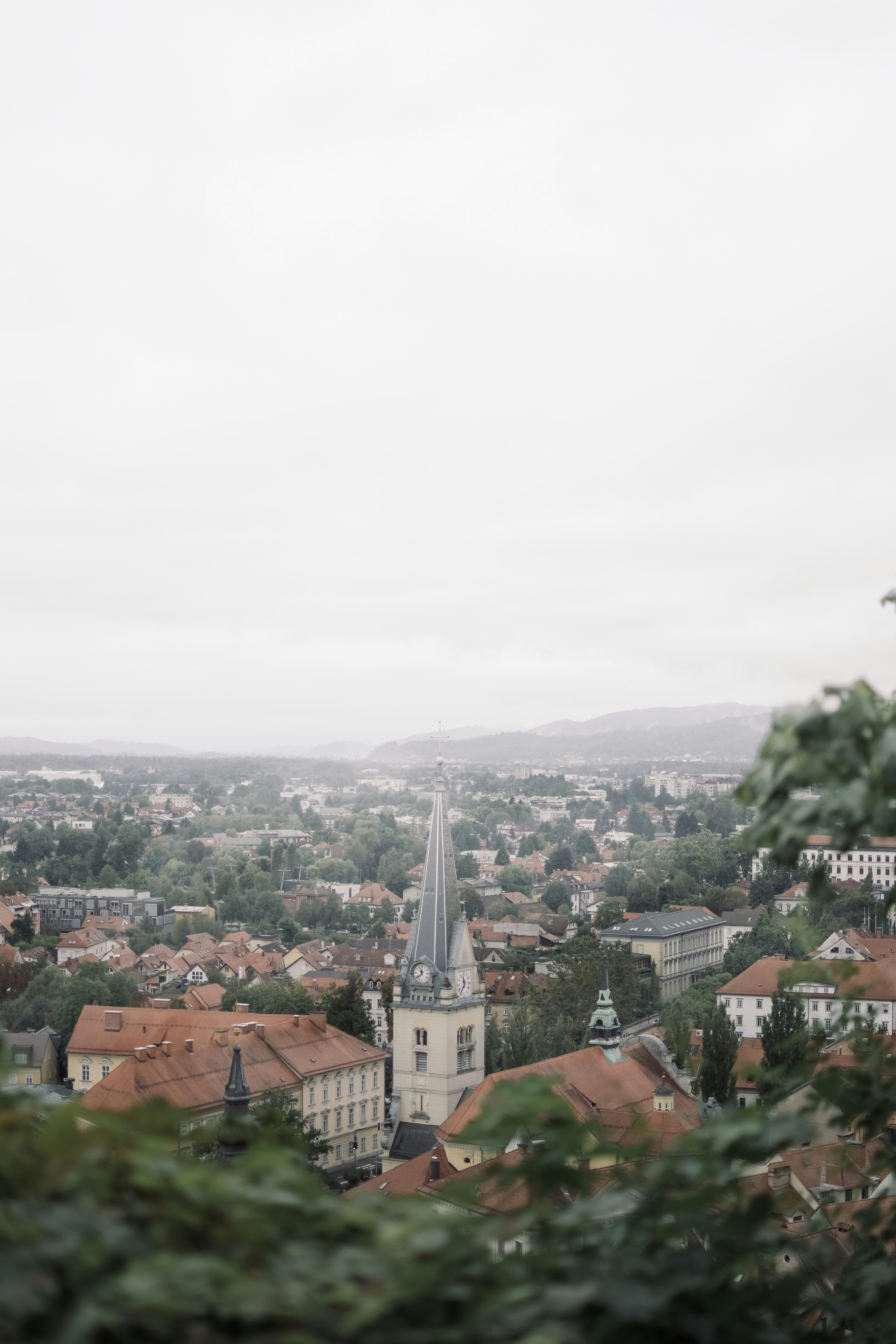 Historic church spire rising above a picturesque town, surrounded by lush greenery and rooftops under a cloudy sky.