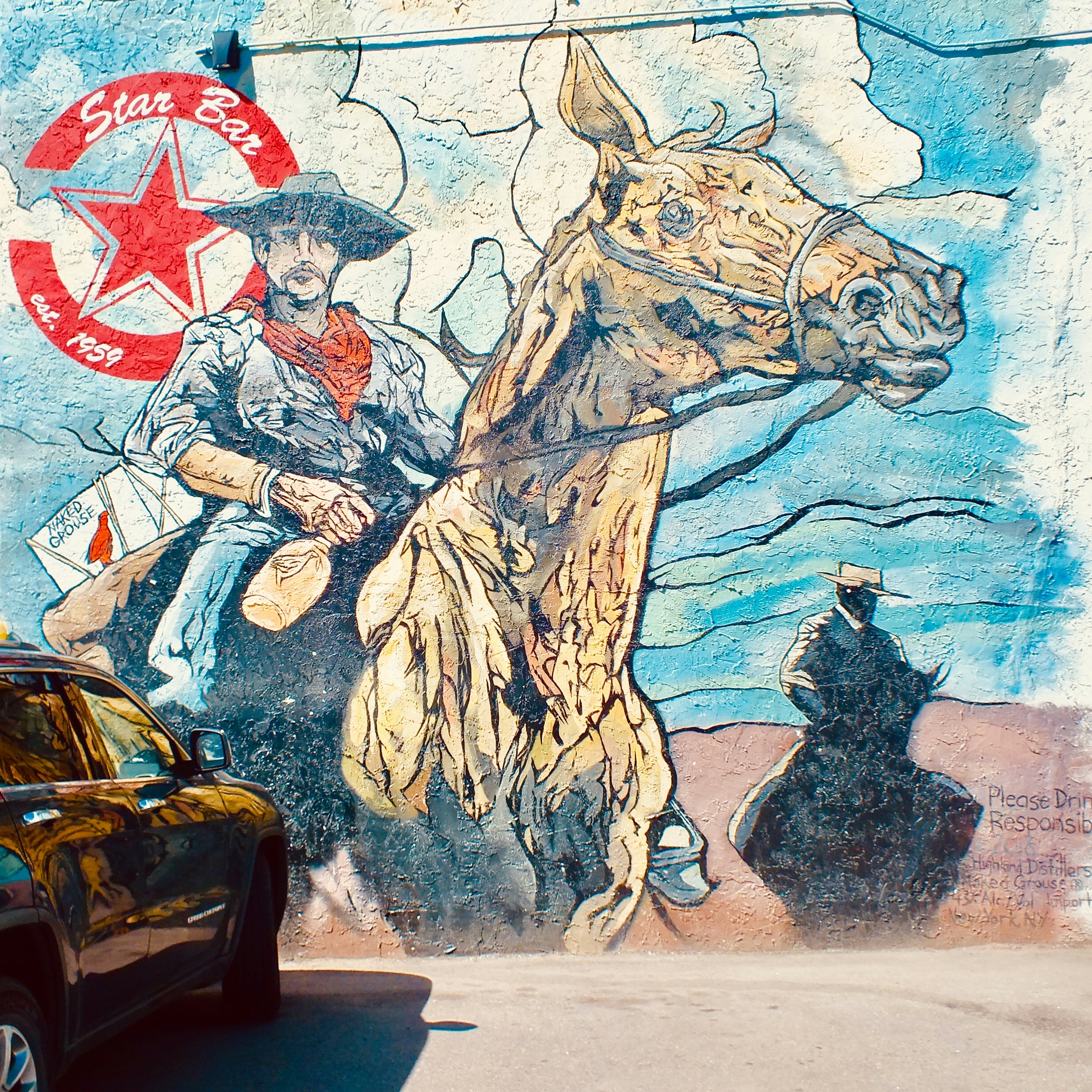 Vibrant mural depicting a cowboy on horseback, surrounded by a vintage star logo and other figures, capturing the essence of Western culture.