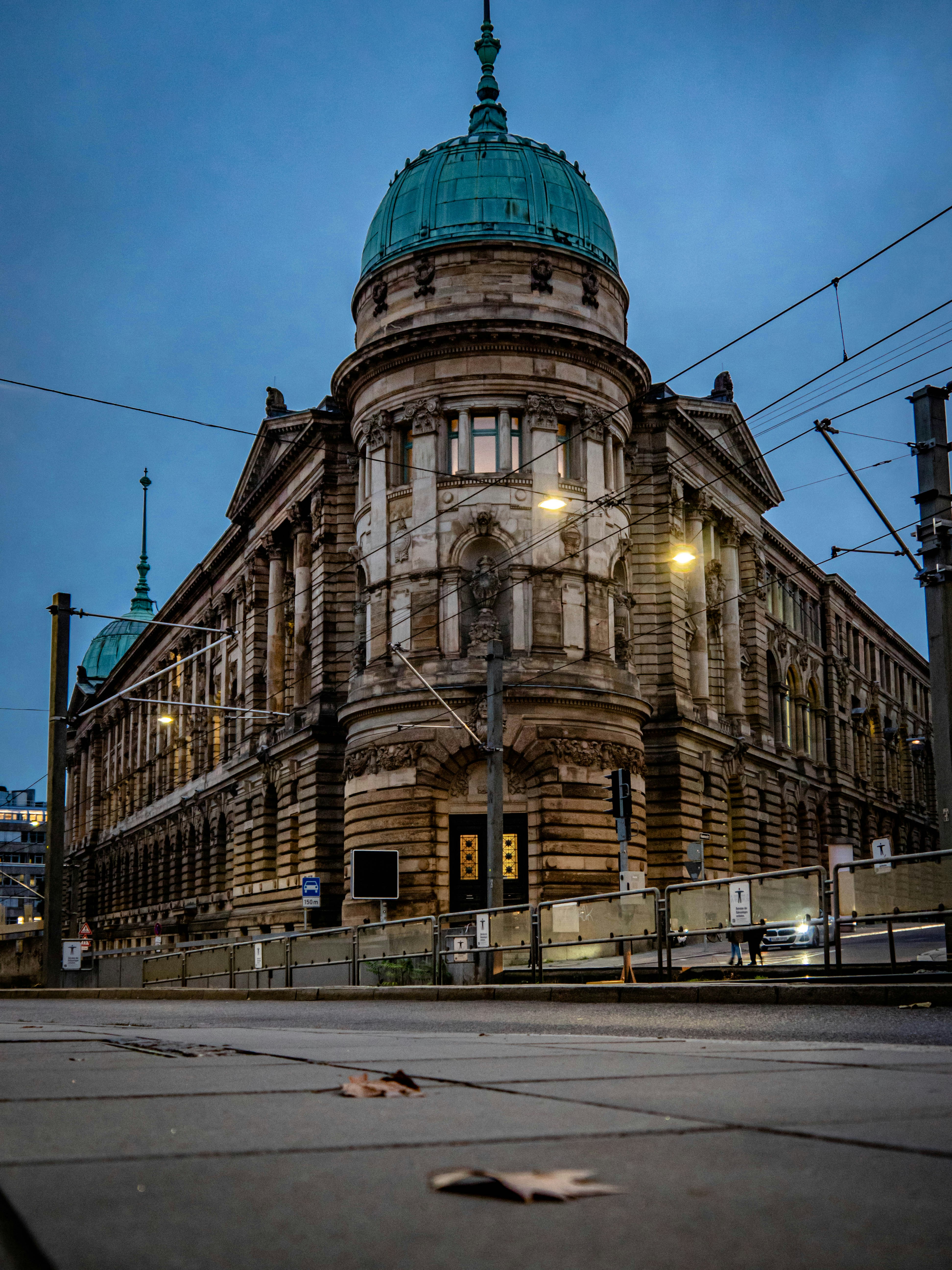 Historic building with a green dome and intricate stonework, illuminated by street lights against a twilight sky.