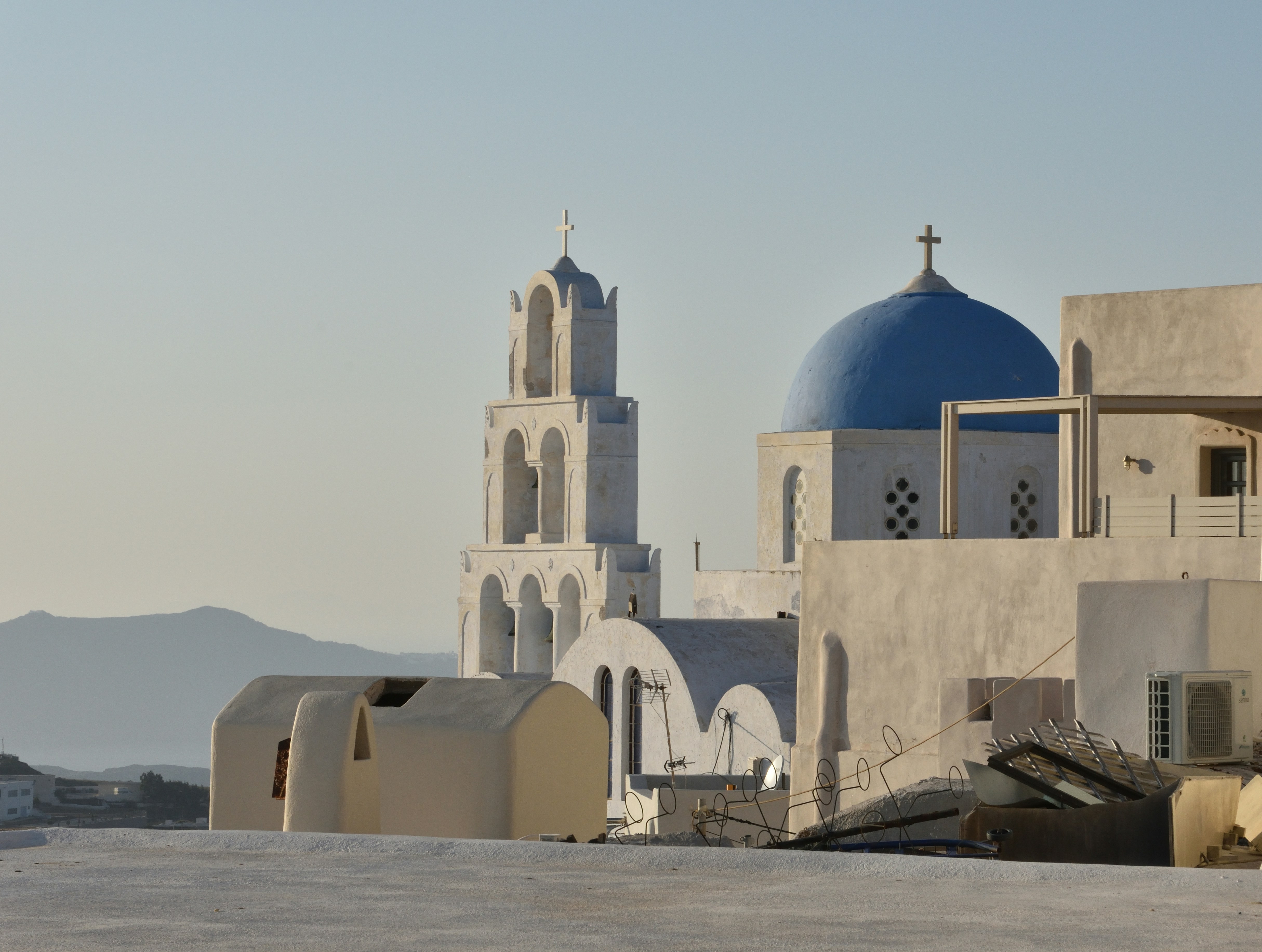Whitewashed buildings with a blue dome and bell tower under a clear sky, showcasing classic Cycladic architecture.