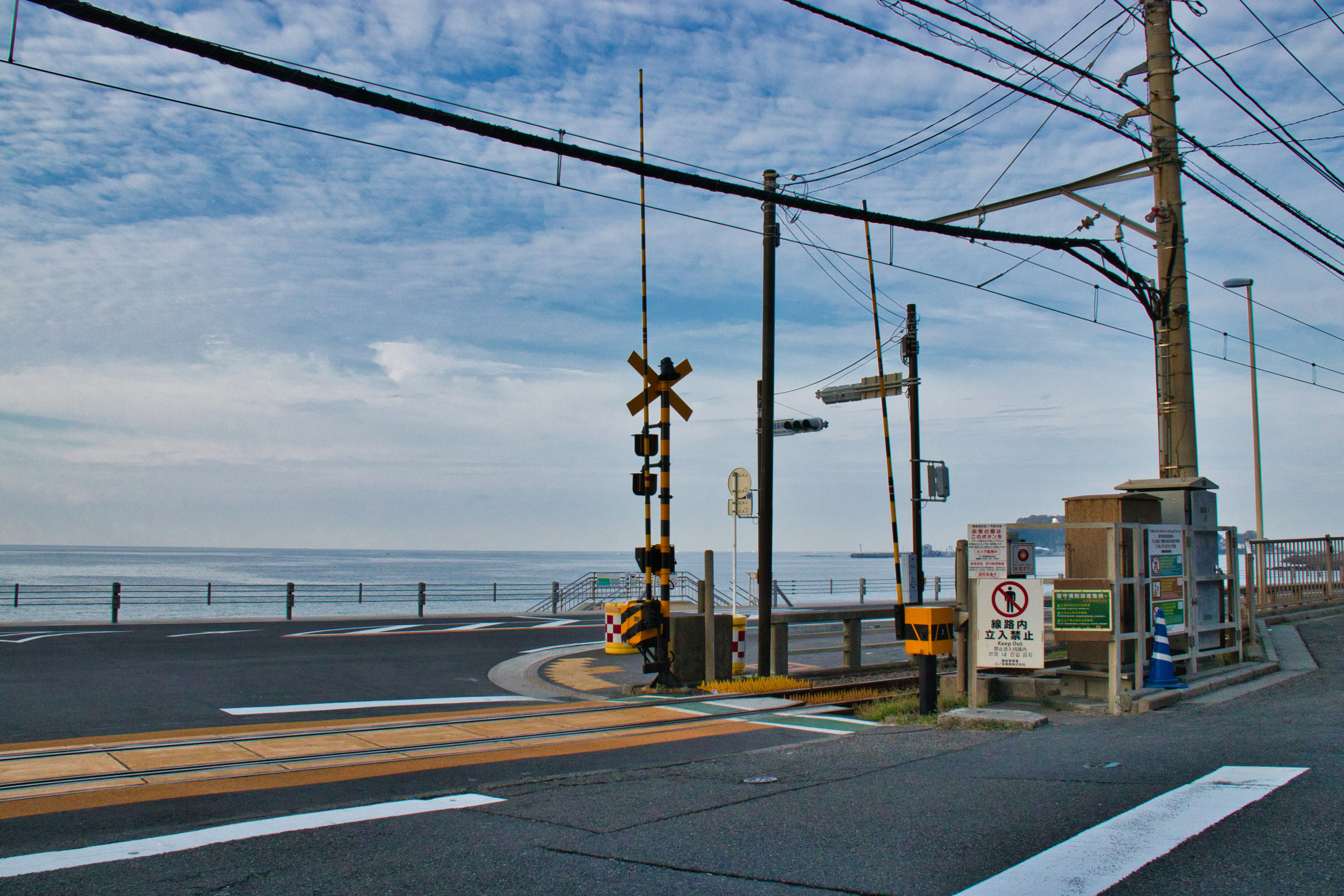 Train crossing signals and road signs near a serene coastal view, highlighting the junction of land and sea.