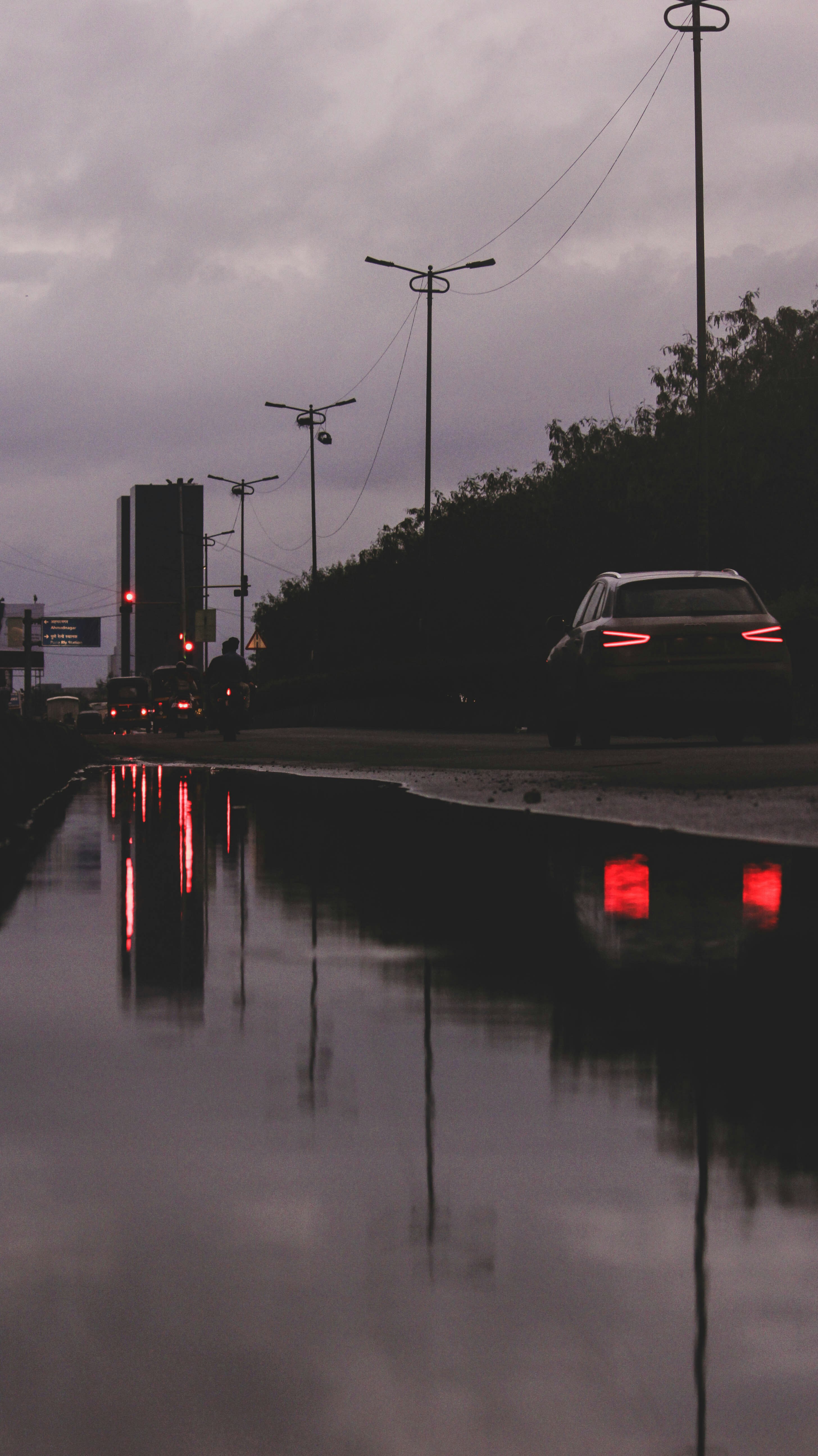 A rainy street scene showcasing the reflections of traffic lights and vehicles in a puddle, creating a moody atmosphere.