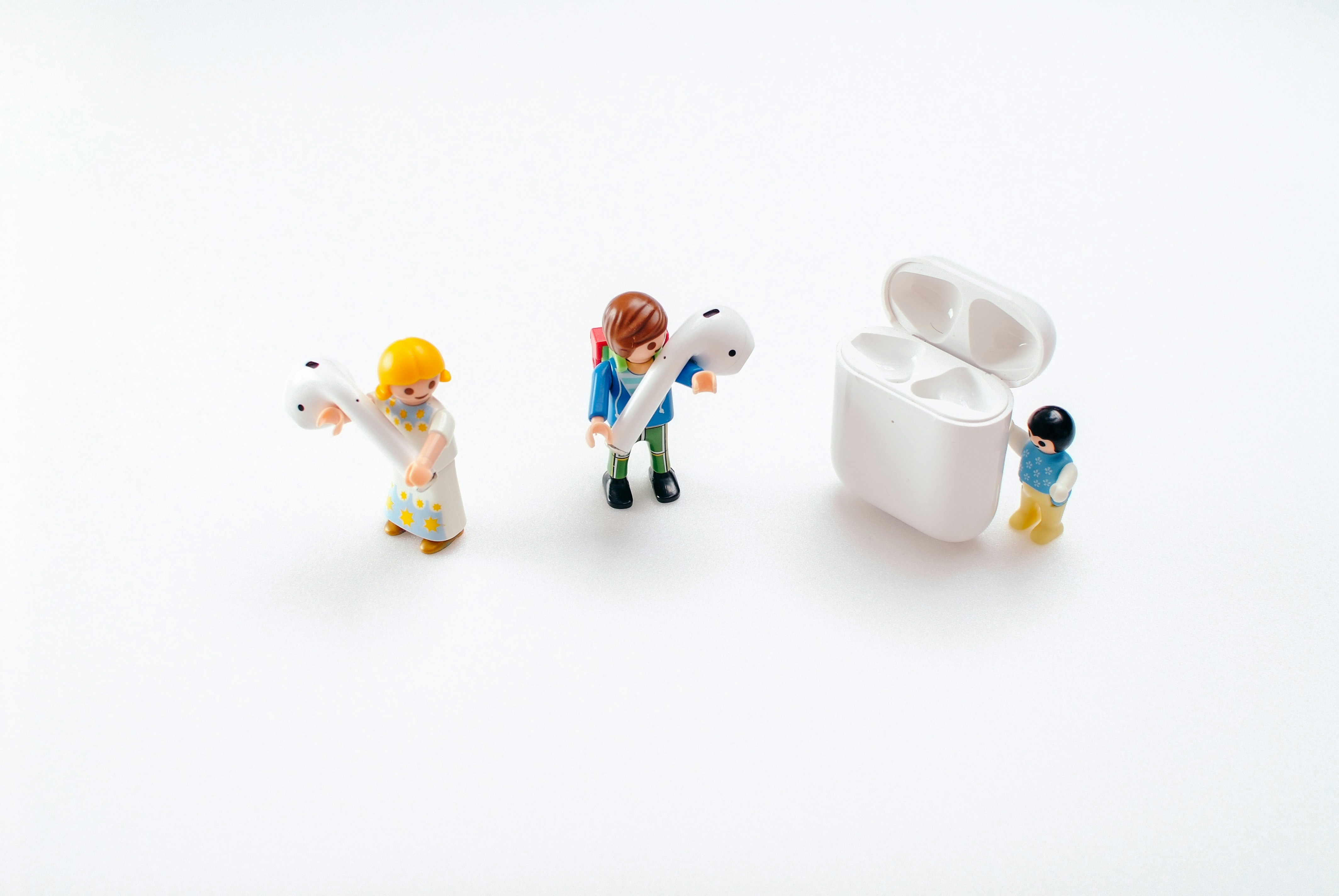 Three playful figures interact with oversized AirPods, showcasing a whimsical blend of technology and imagination.