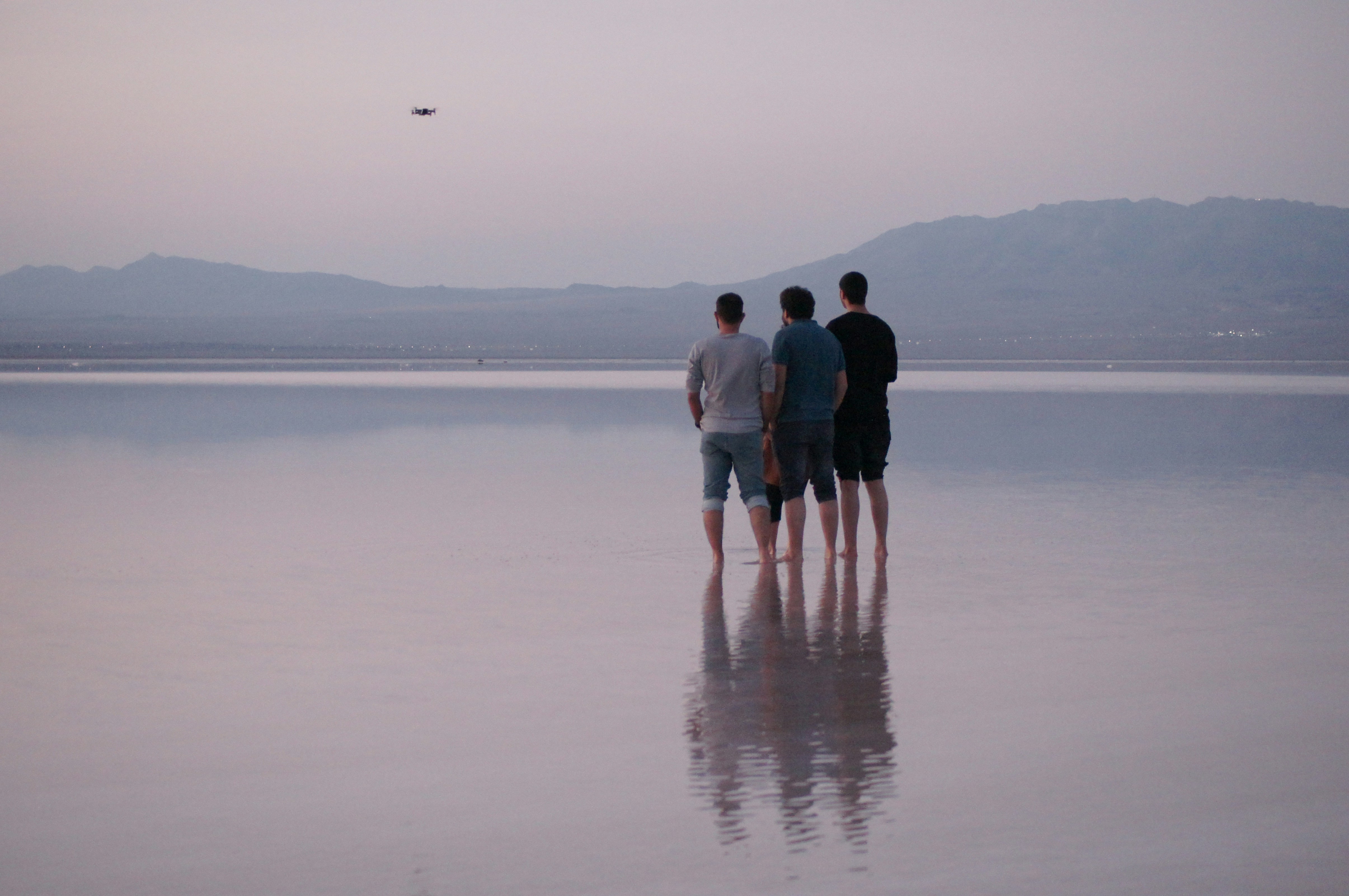 Three figures at the shoreline: a quiet horizon between water and mountains