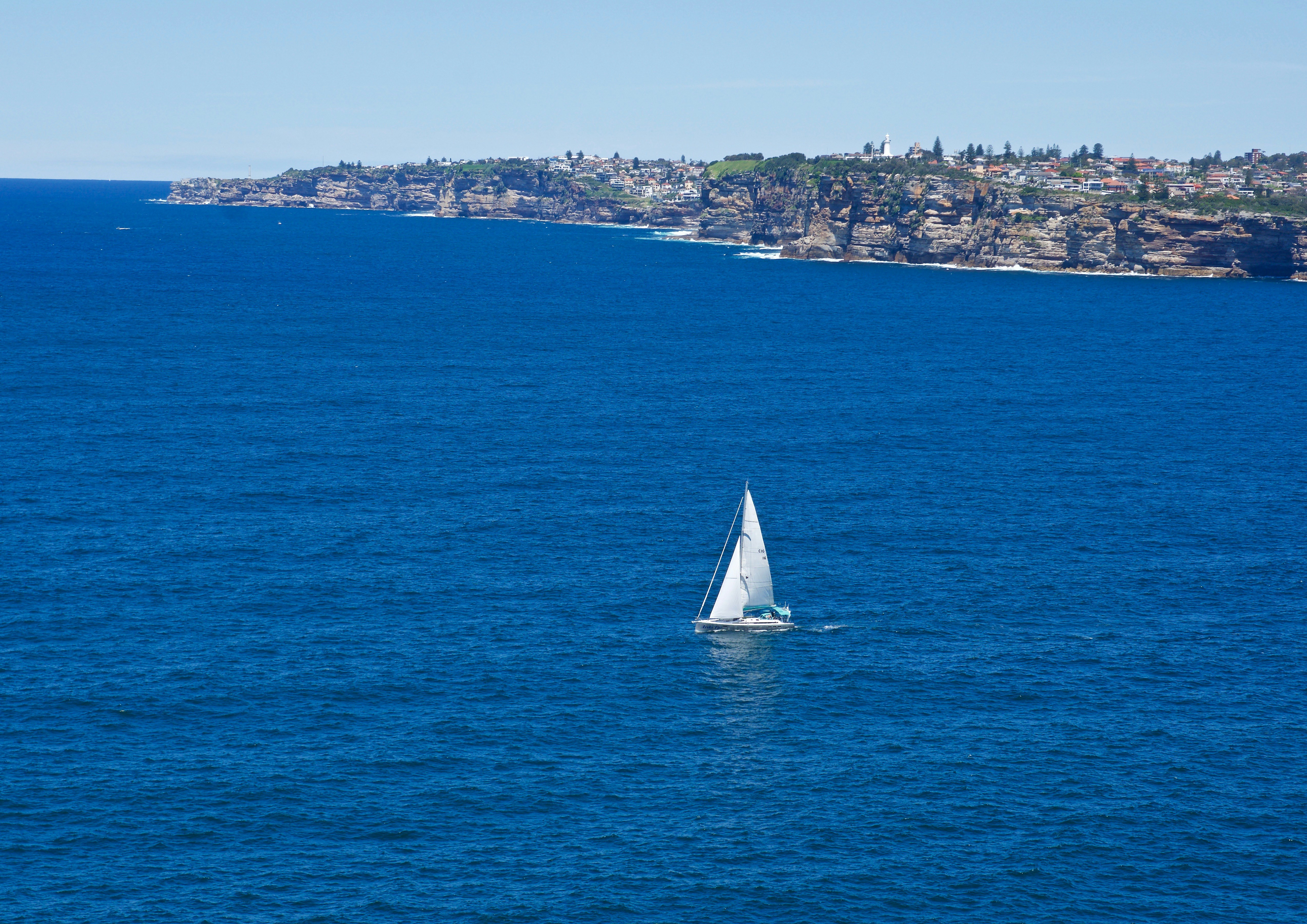 Sailboat gliding across deep blue waters with a coastal landscape in the background, showcasing a serene maritime scene.