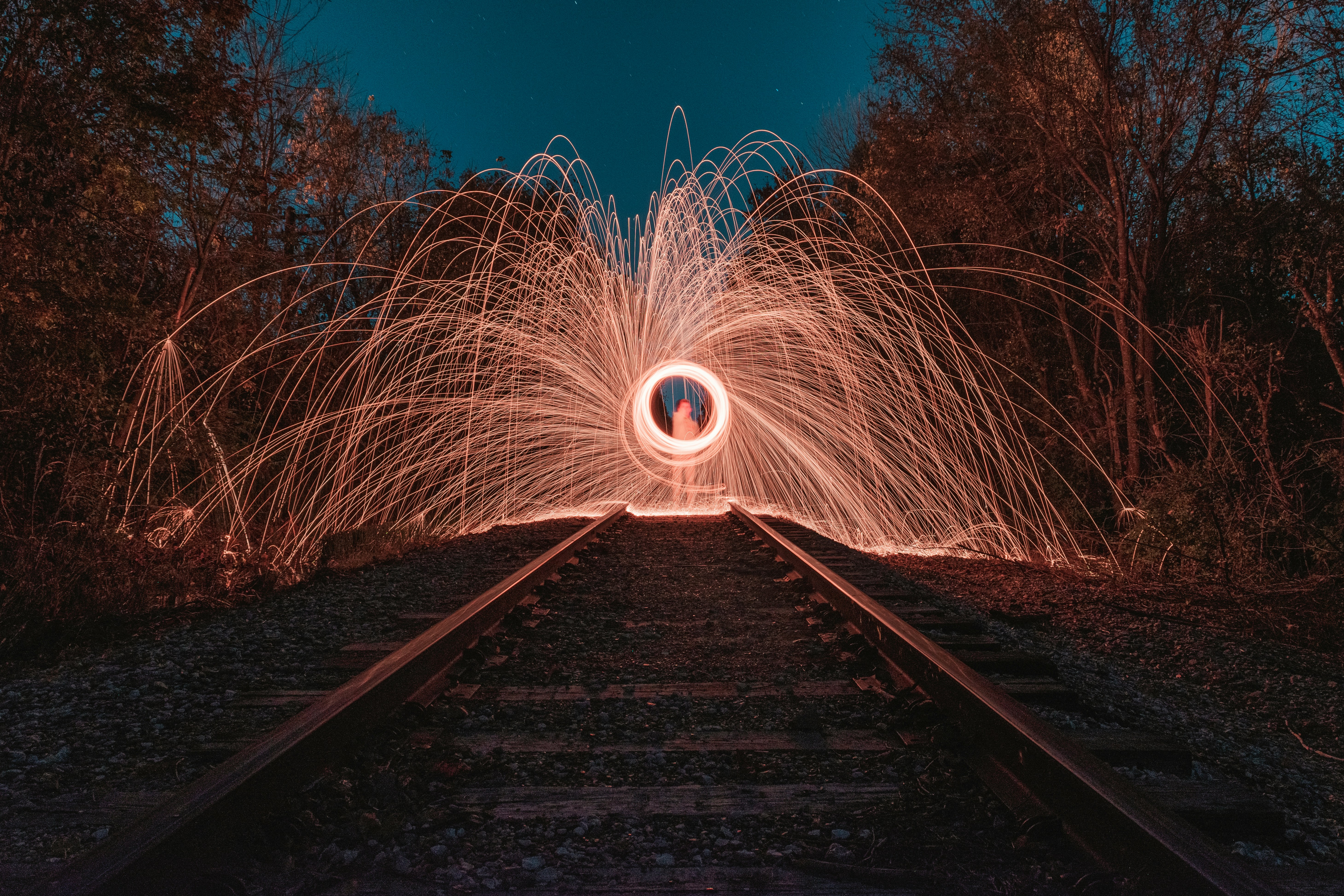 Long exposure of steel wool spinning on railway tracks under a starry night sky.