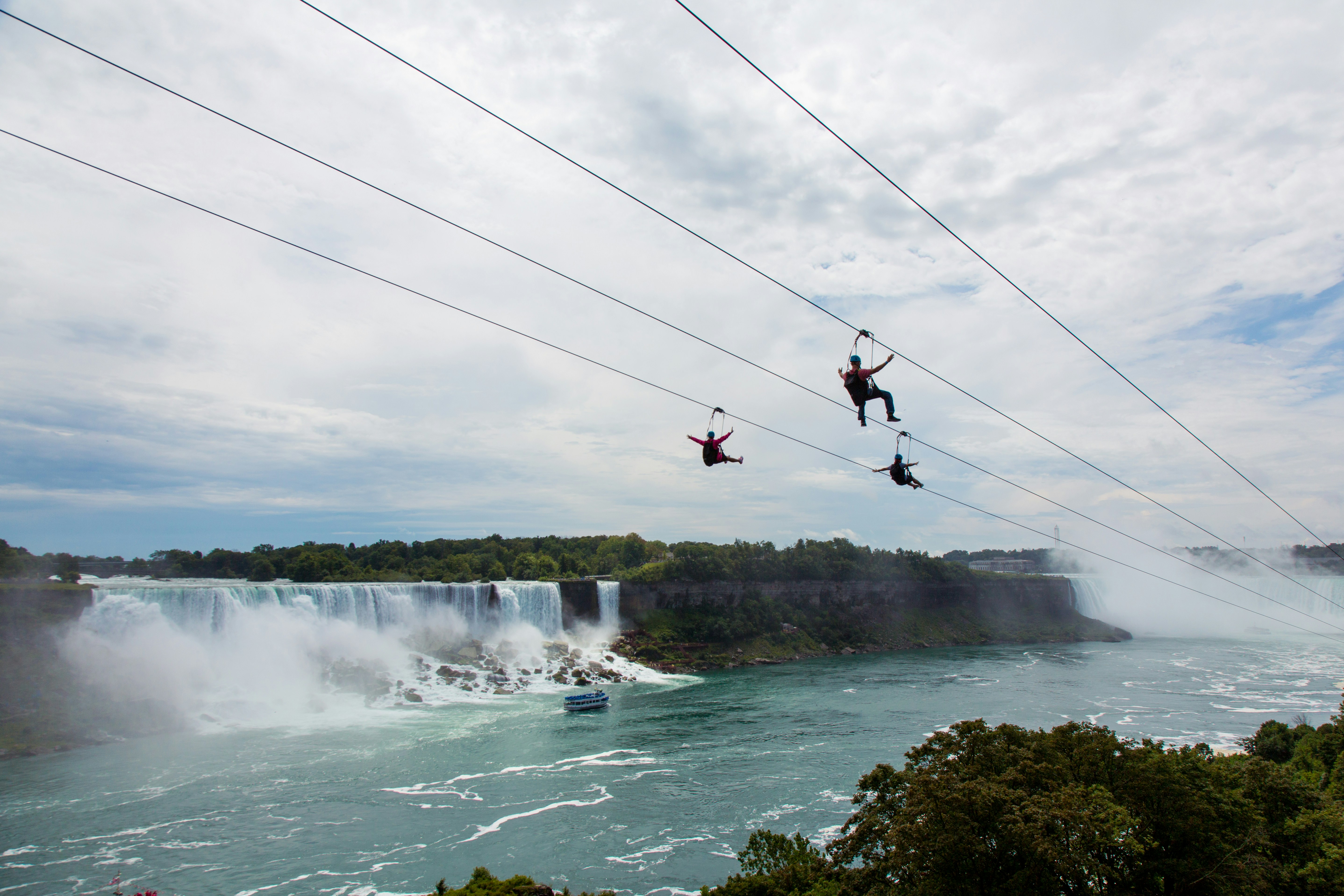 Zip liners glide above Niagara Falls with mist rising in the background.