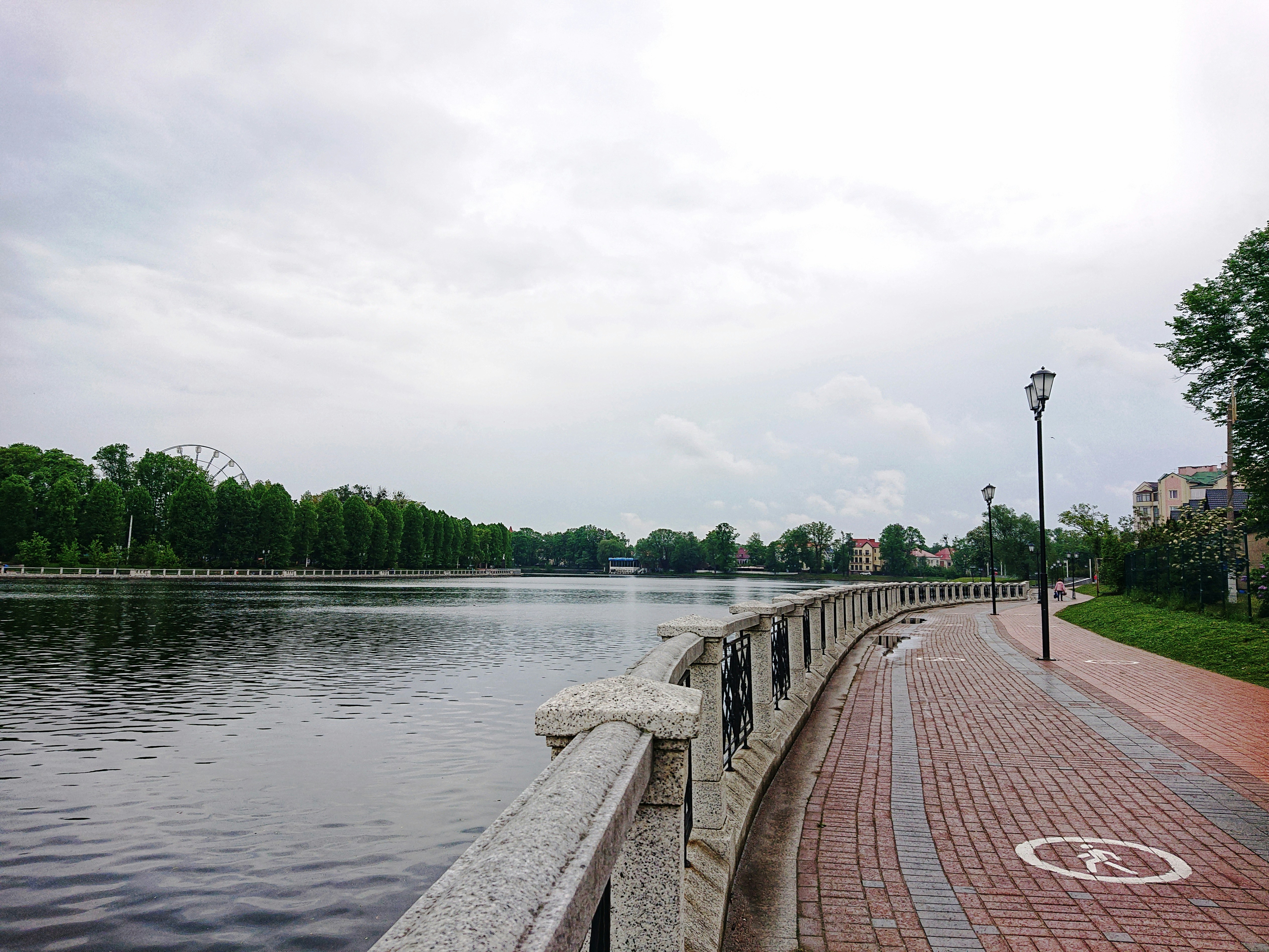 Brick walkway curves along a tranquil riverbank under an overcast sky.