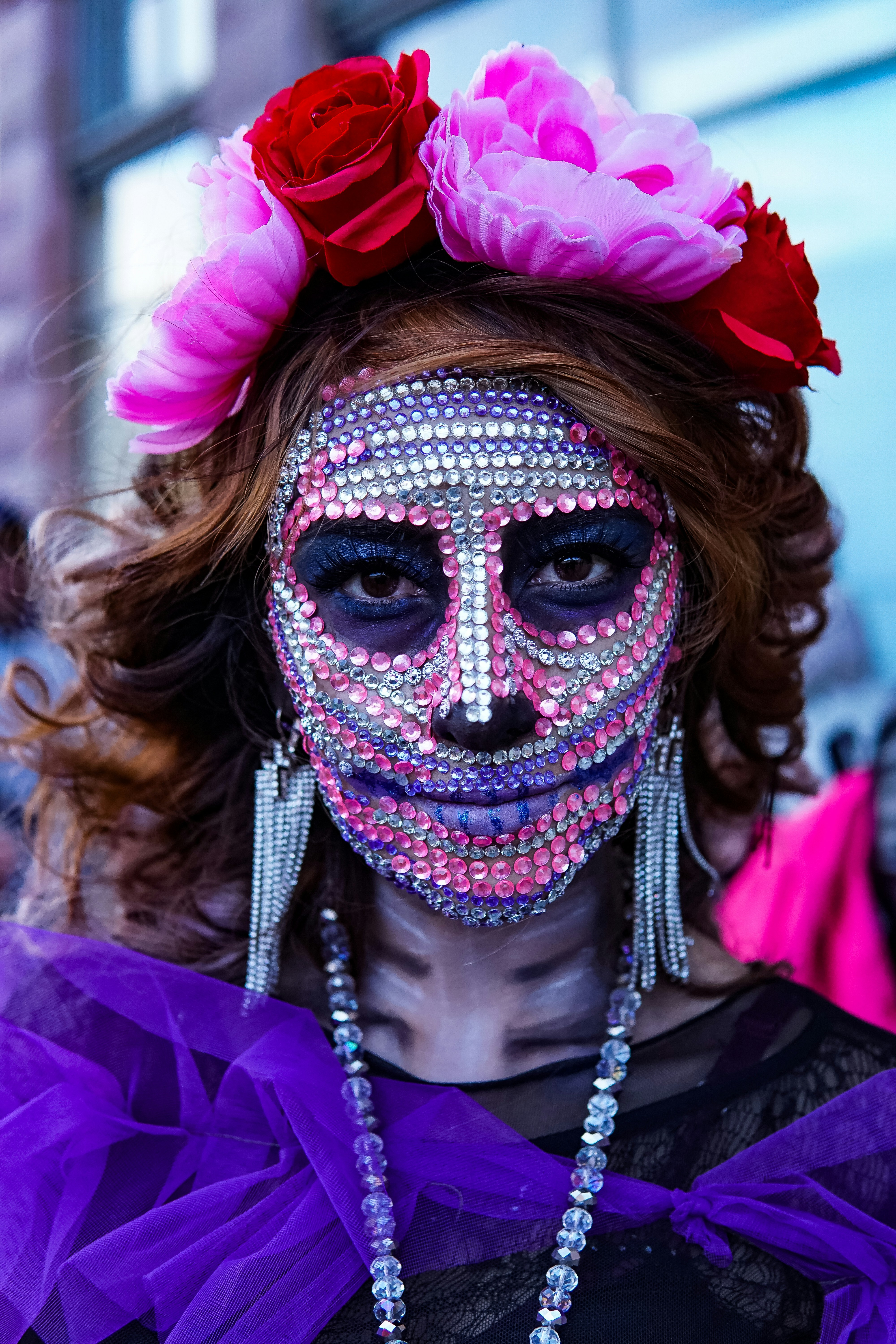 Person adorned with colorful face jewels and floral headpiece during Día de Muertos celebration.