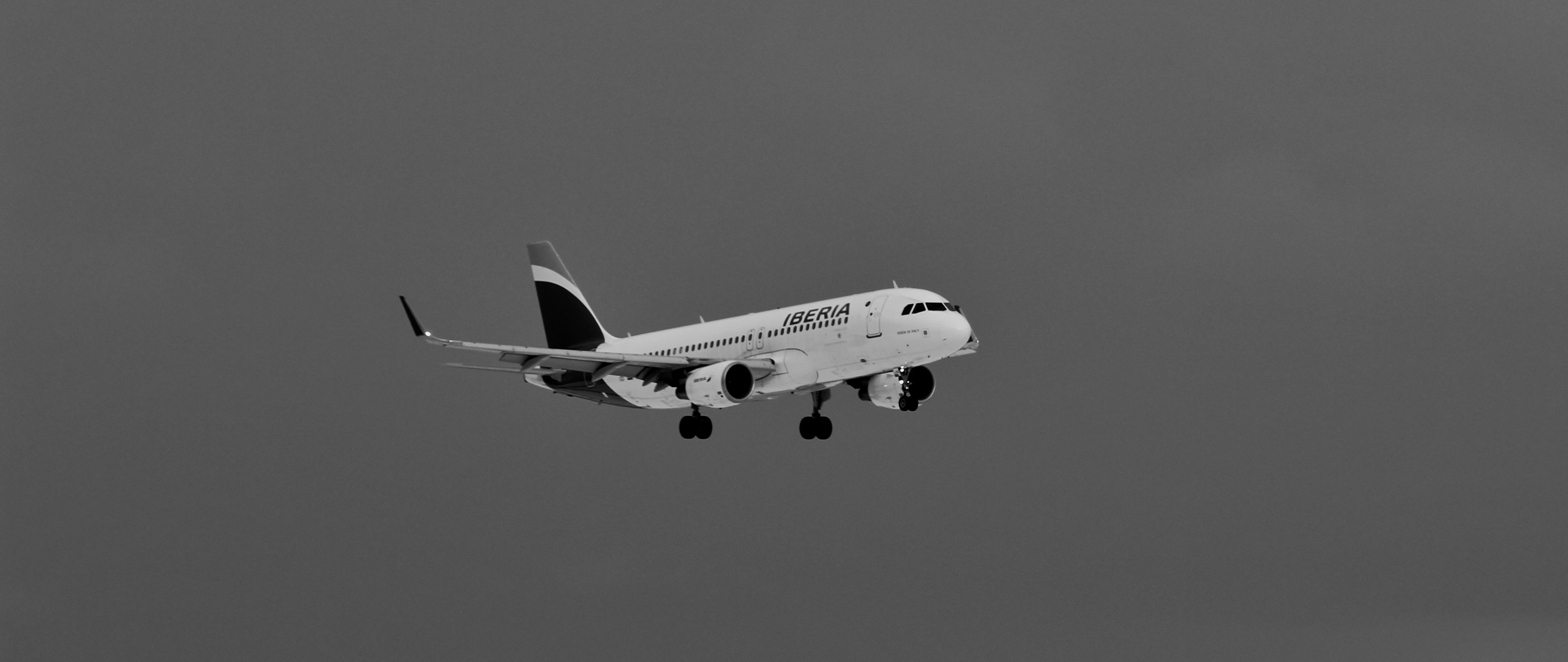 Commercial aircraft gliding through a moody sky, captured in monochrome. The image emphasizes the aircraft's sleek design against a dramatic backdrop.