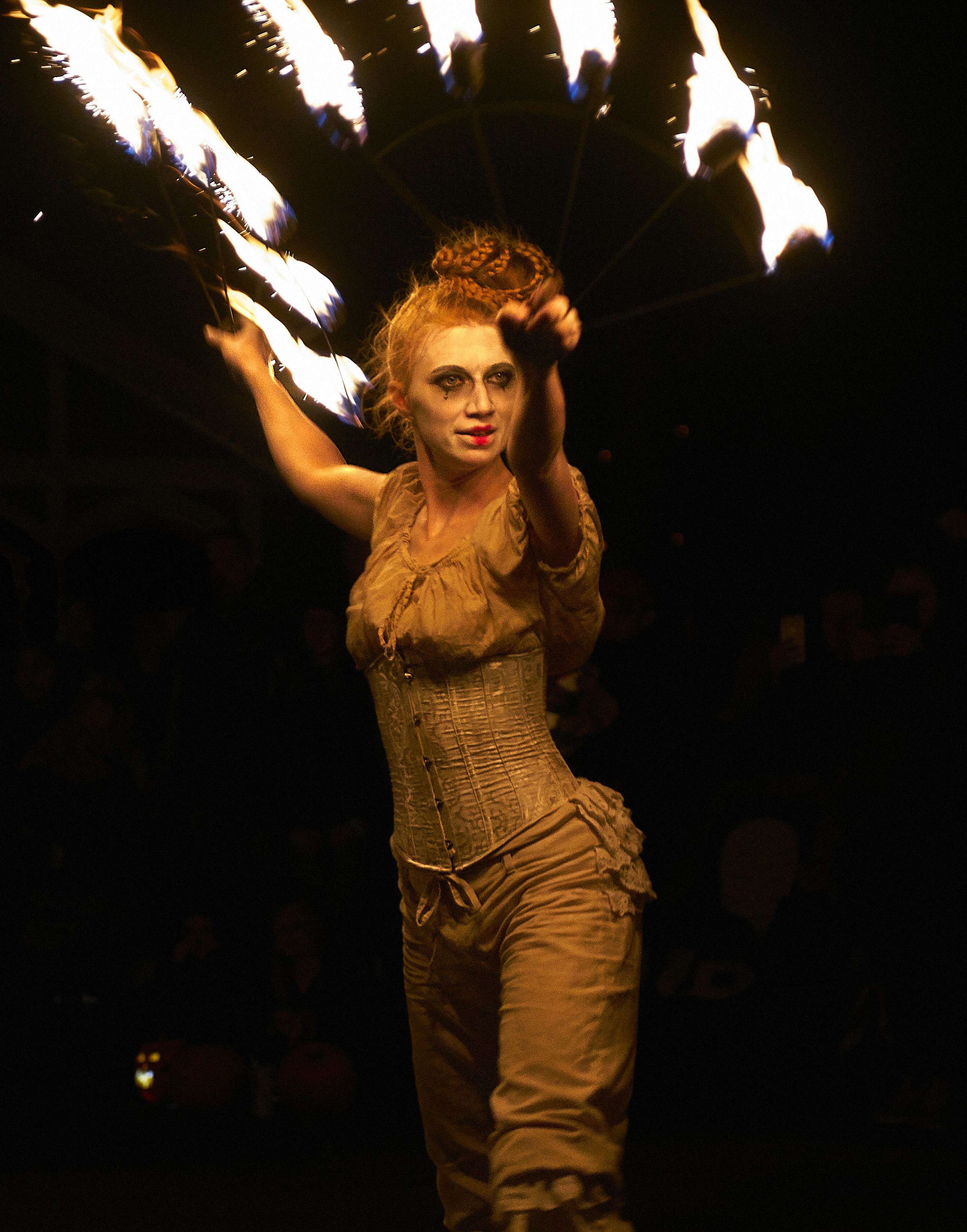 Fire performer skillfully twirling flaming poi in a darkened venue, showcasing grace and intensity.