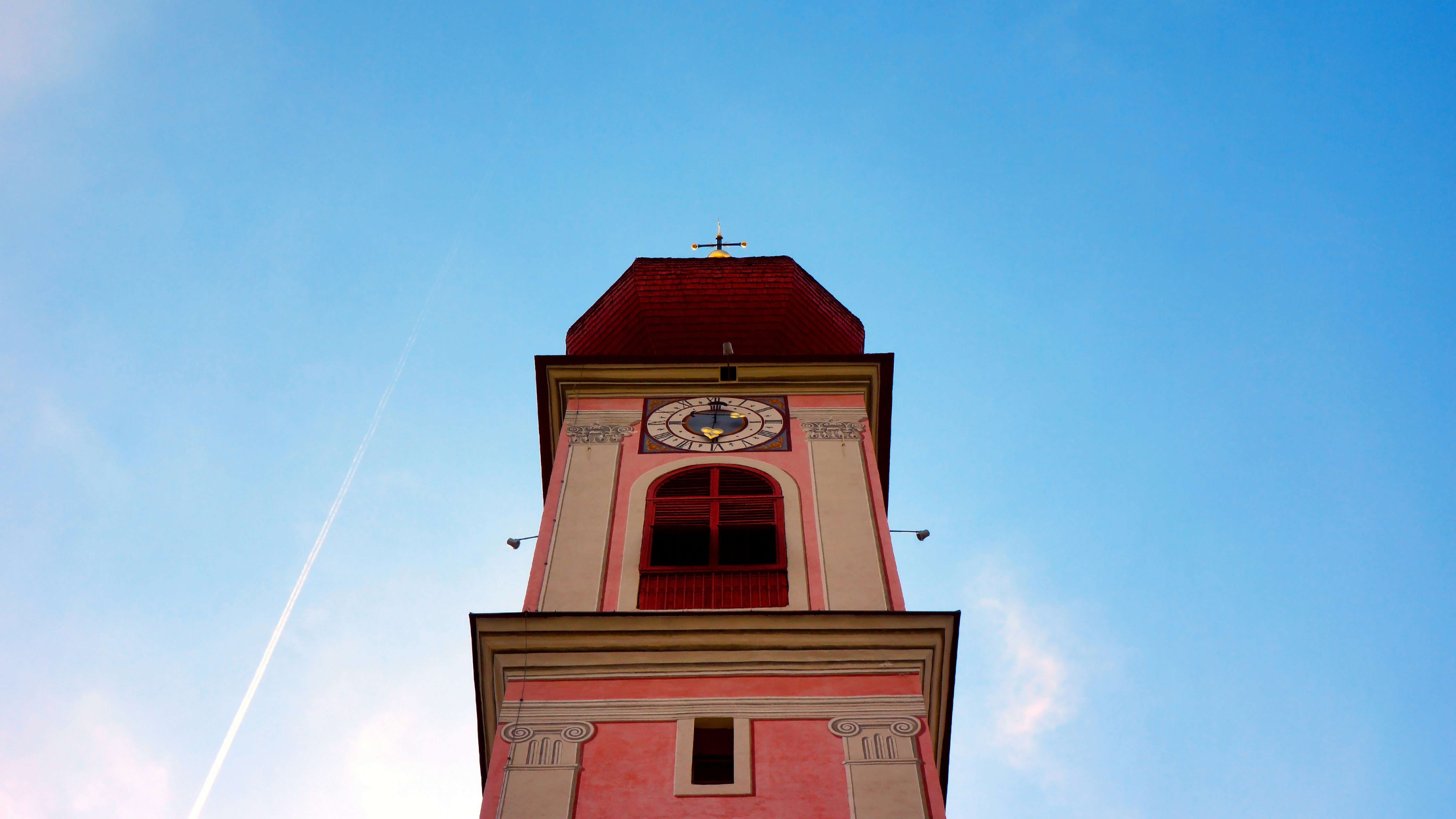 Tall clock tower with a red roof and intricate detailing against a clear blue sky.