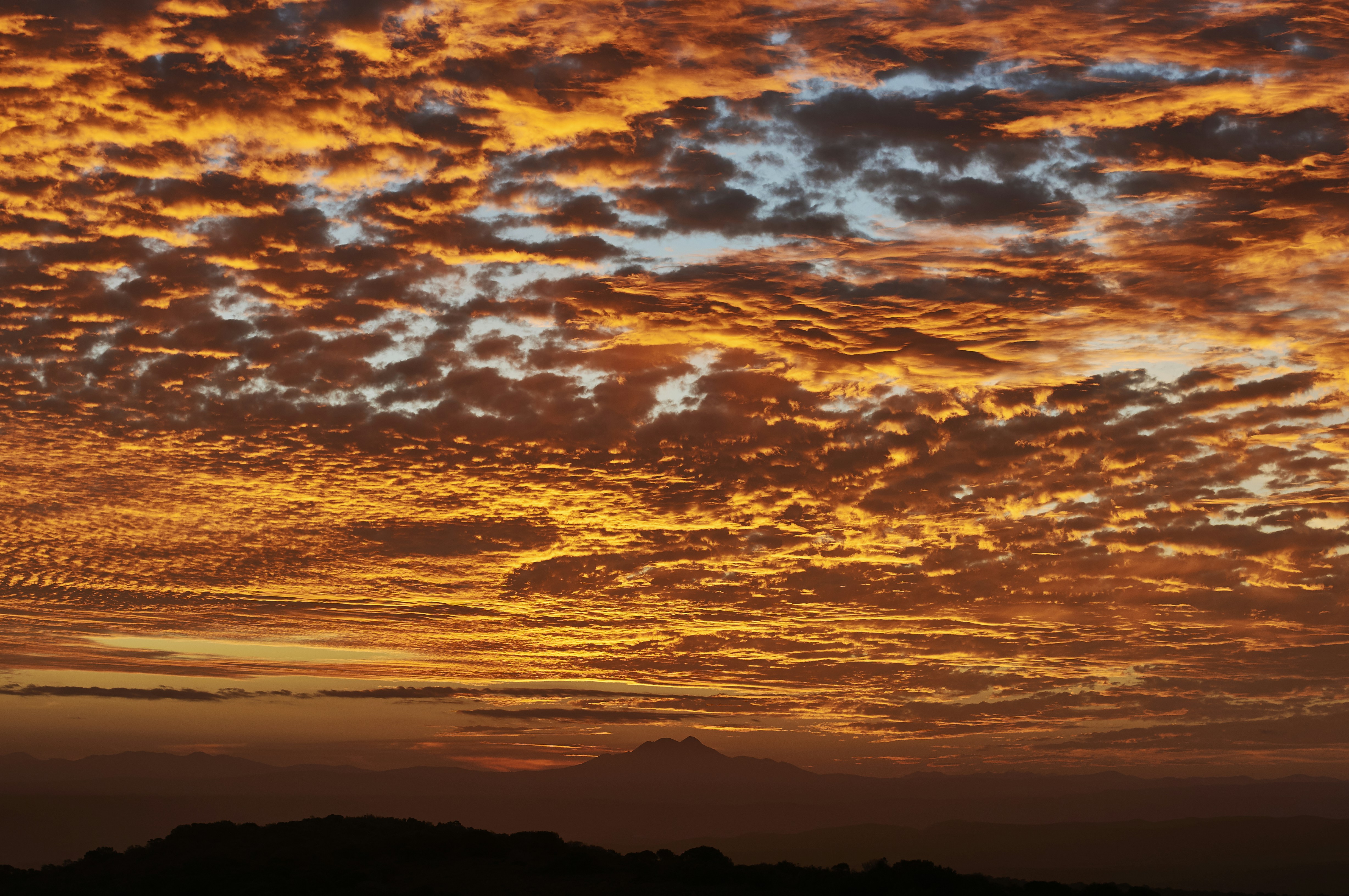 Vibrant orange and blue sunset with textured clouds over a silhouette of distant hills.