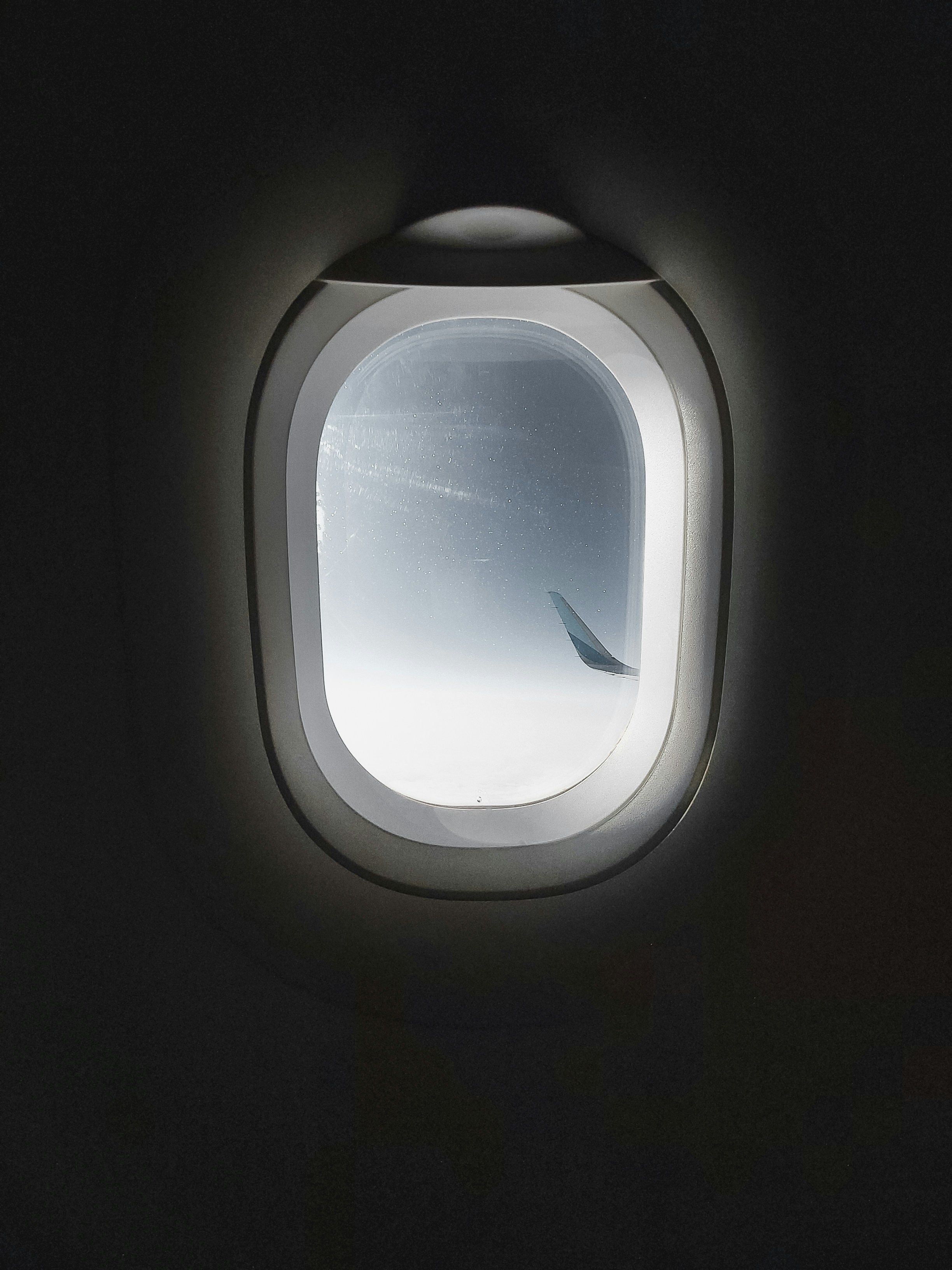 View through an airplane window showcasing a wingtip against a backdrop of clouds and sky.