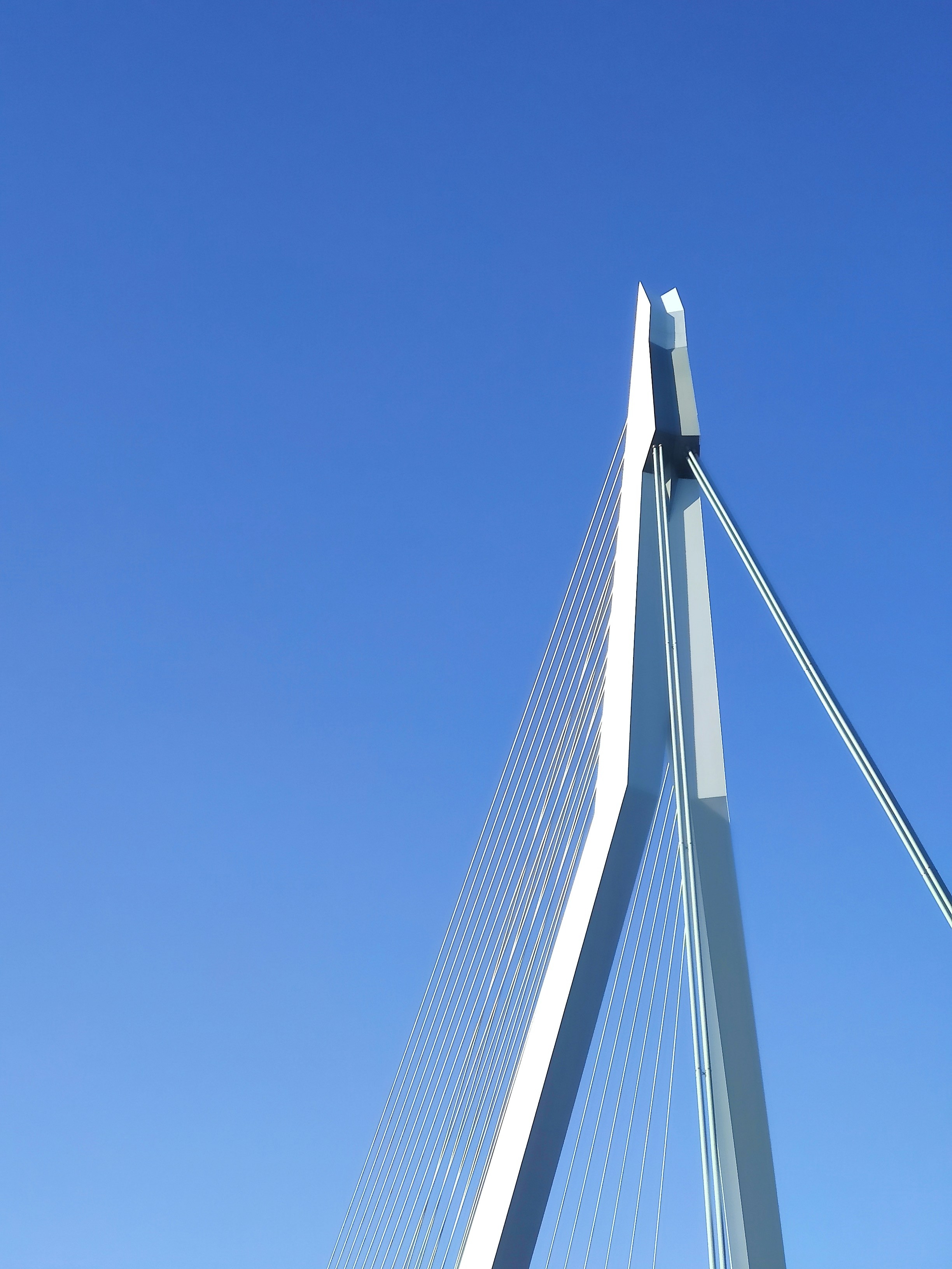 Cable-stayed bridge pylon rises against a clear blue sky, with taut cables fanning from the apex.