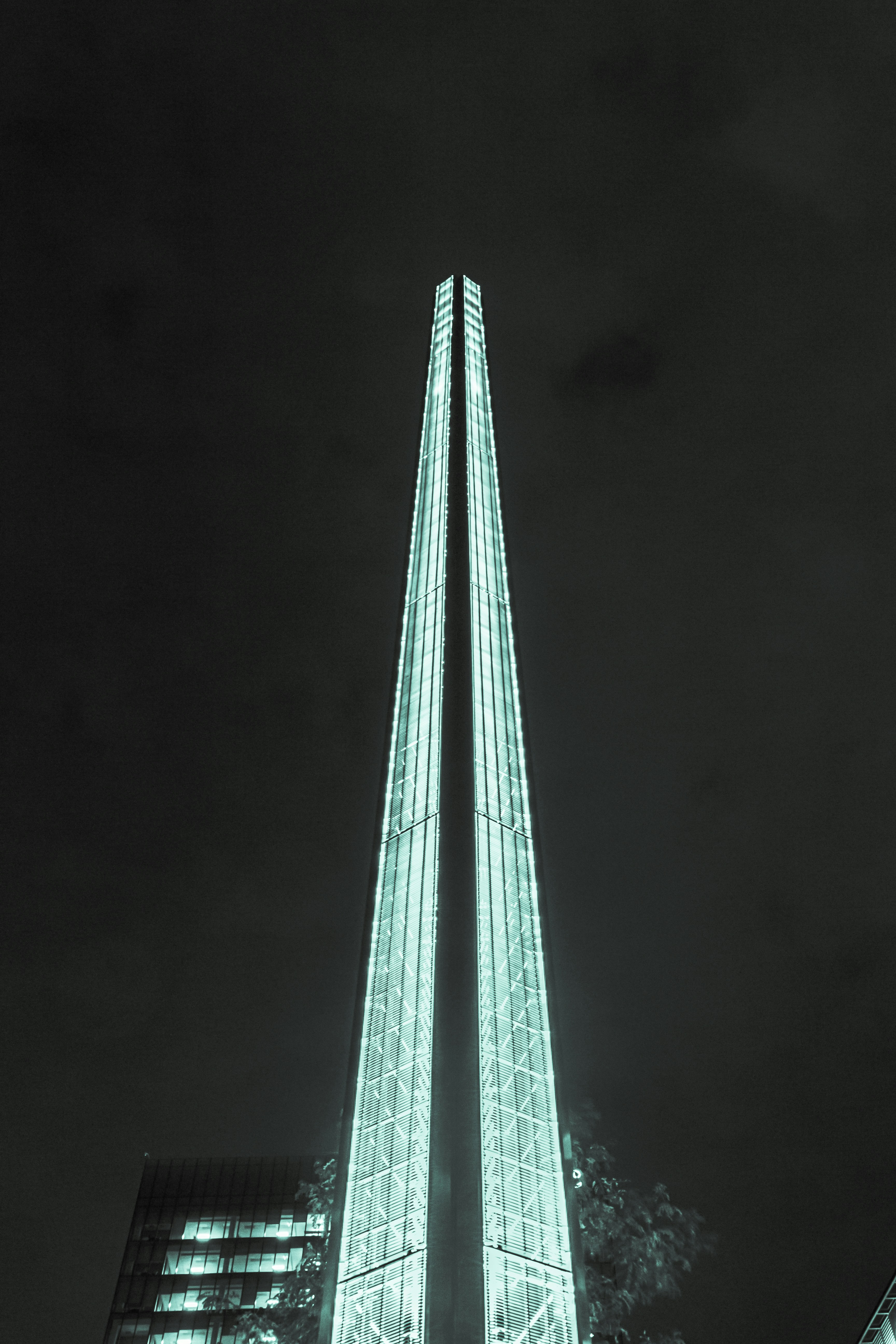 Illuminated tower reaching towards a darkened sky, showcasing sleek architectural lines amidst urban surroundings.