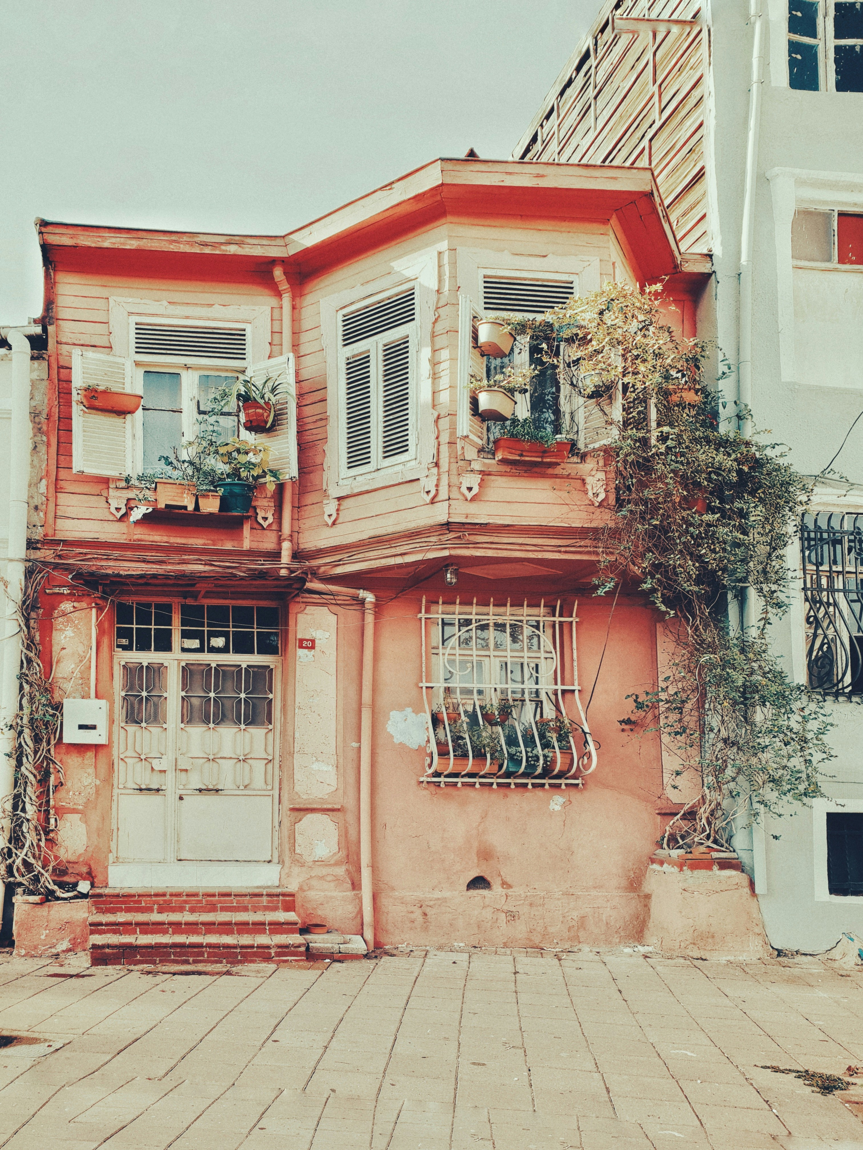 Peach-toned two-story house with a protruding bay window and shuttered upper windows, ivy clinging to the facade, and potted plants on the balcony.
