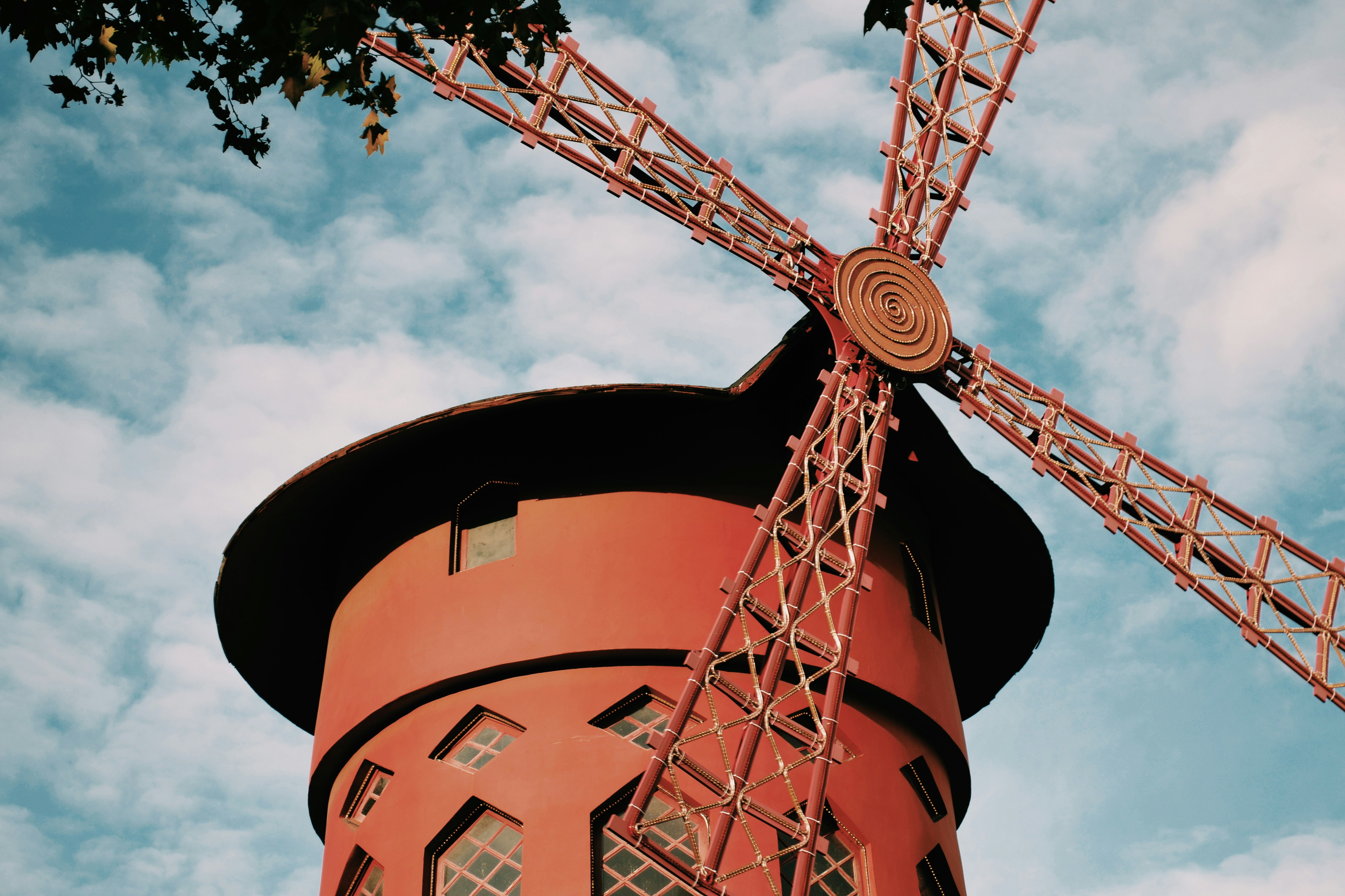 Red windmill with intricate lattice blades against a backdrop of fluffy clouds.