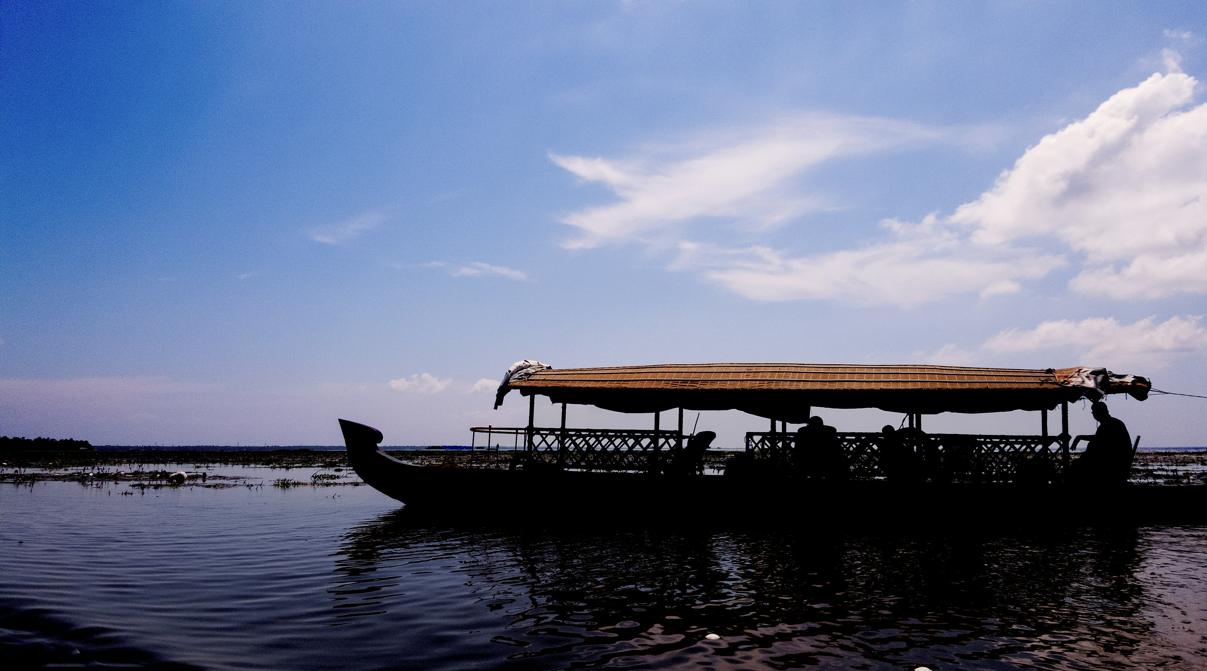 Silhouette of a traditional boat gliding over calm waters under a vast blue sky with wispy clouds.
