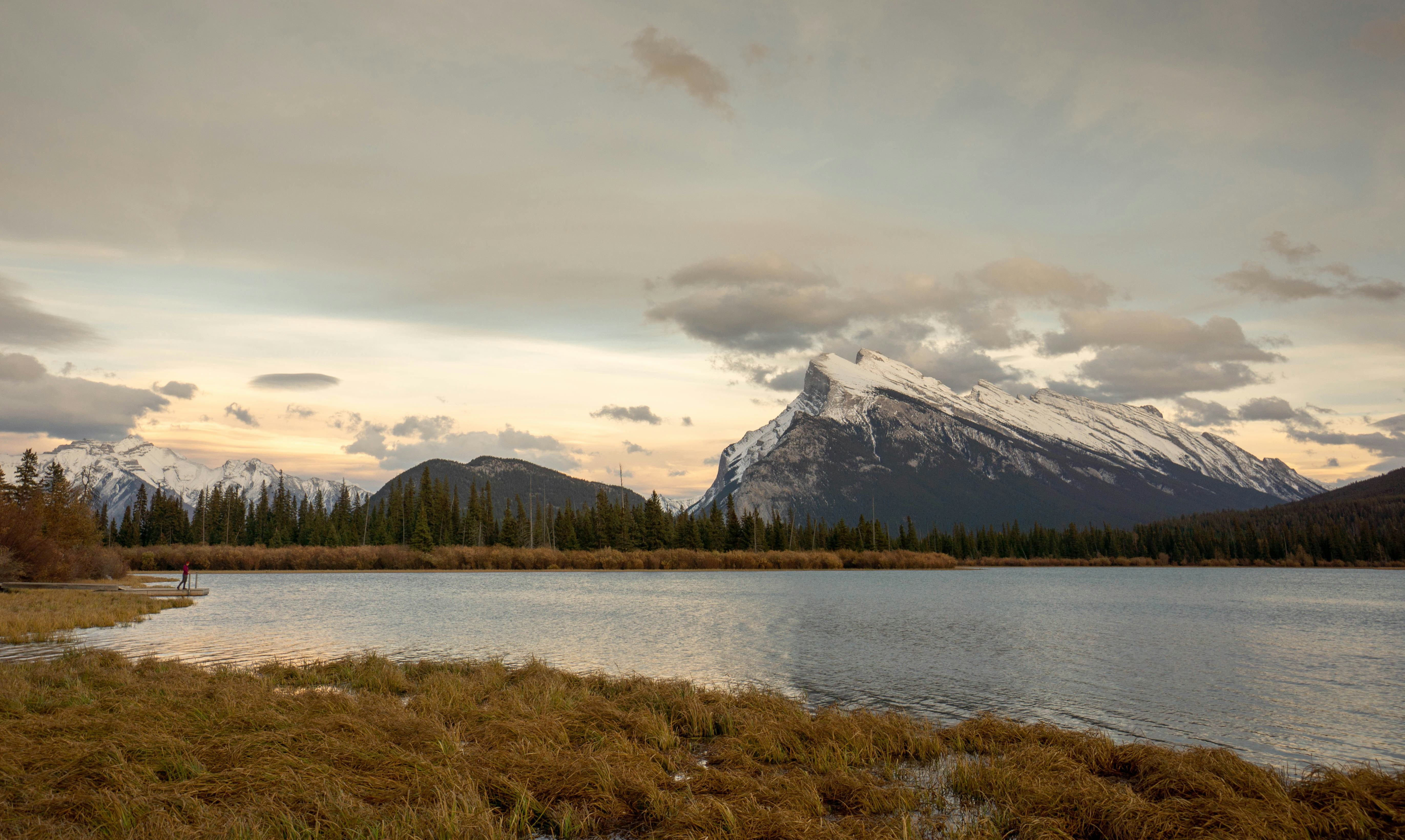 Snow-capped mountain reflected in tranquil lake under a cloudy evening sky.