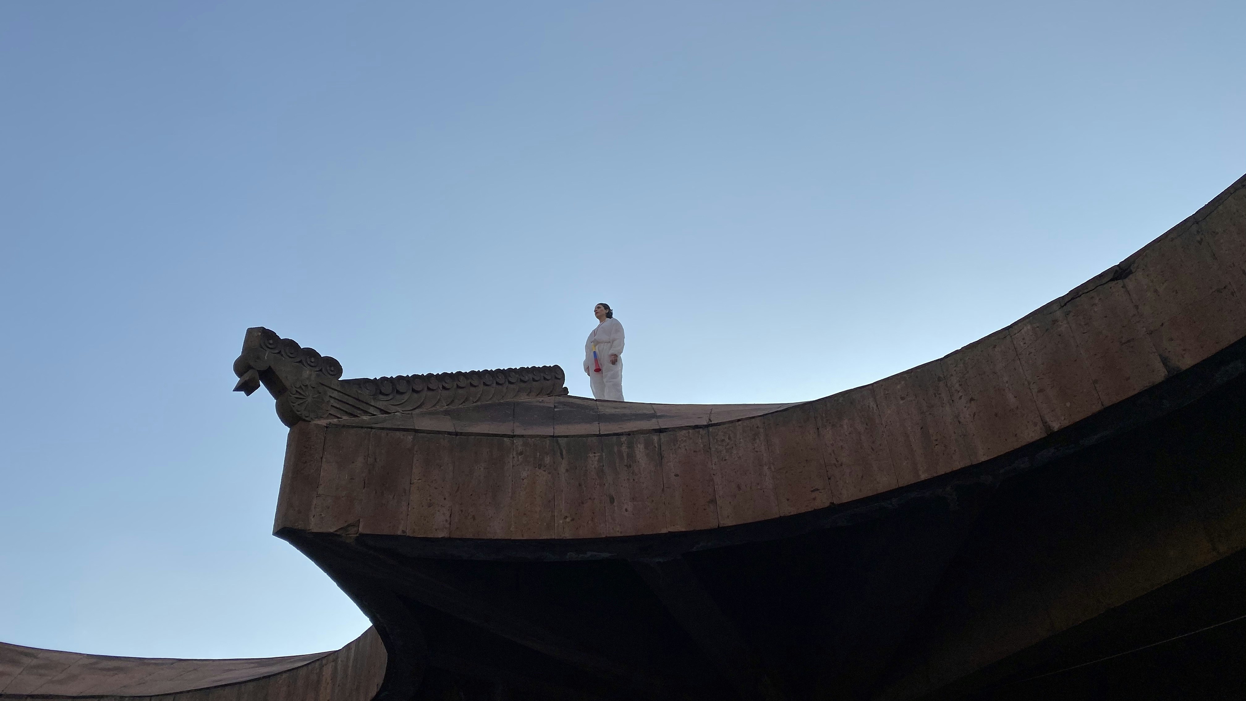 Person standing atop a curved concrete structure against a clear blue sky.
