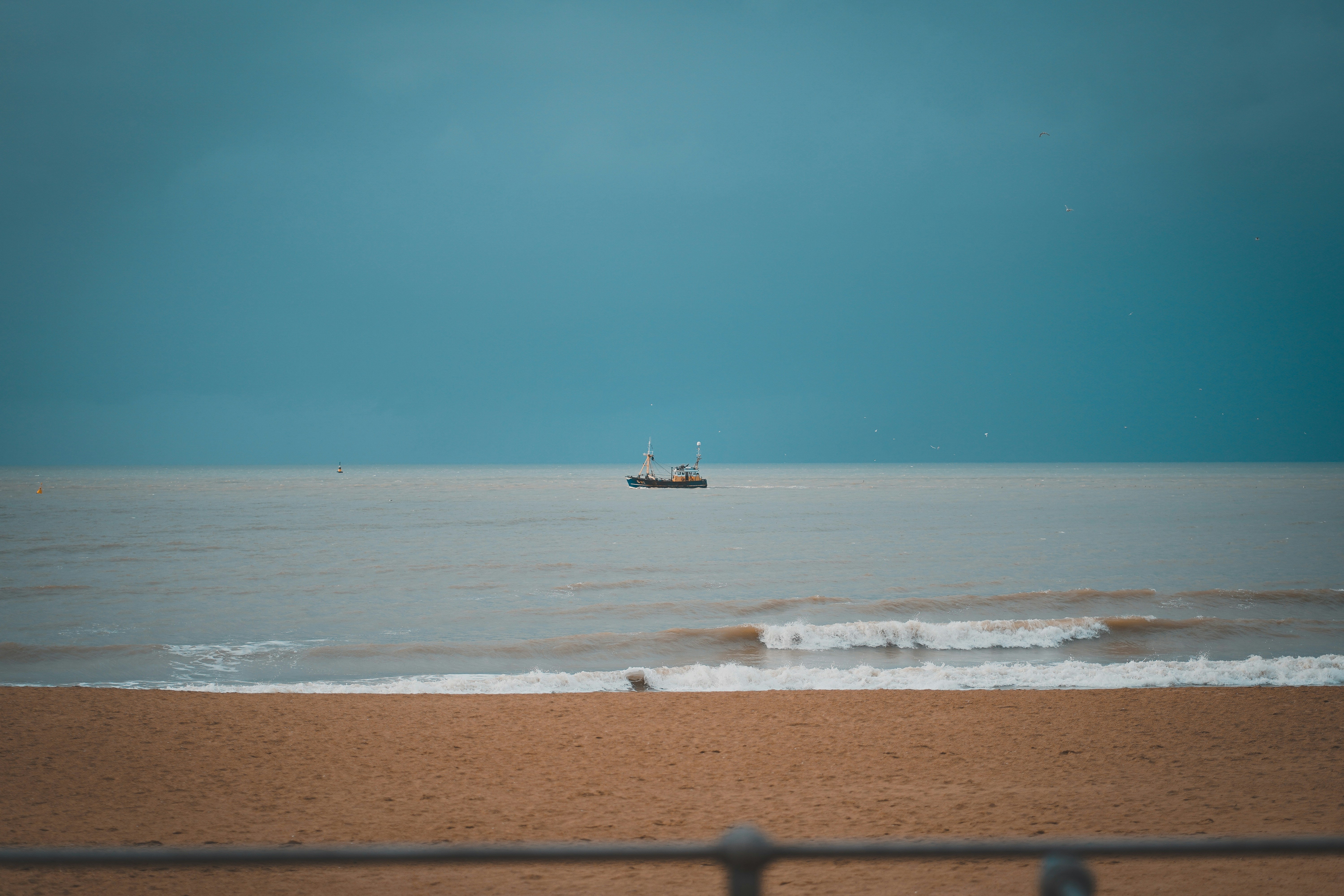 Fishing boat gently bobbing on calm waters under a moody sky, with sandy beach in the foreground. 