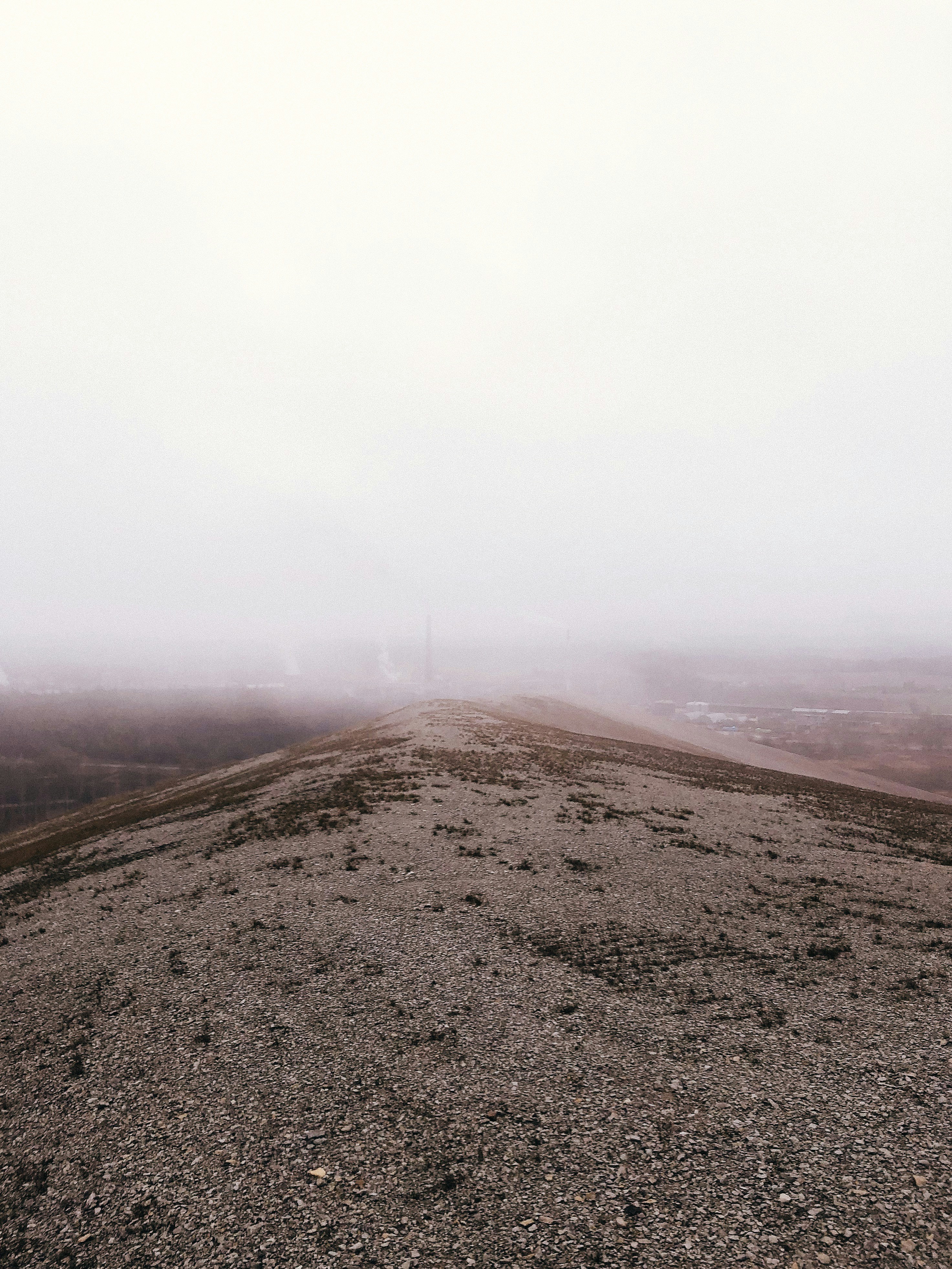 A gravel-covered ridge disappears into a dense fog, creating a sense of mystery and solitude in the landscape.