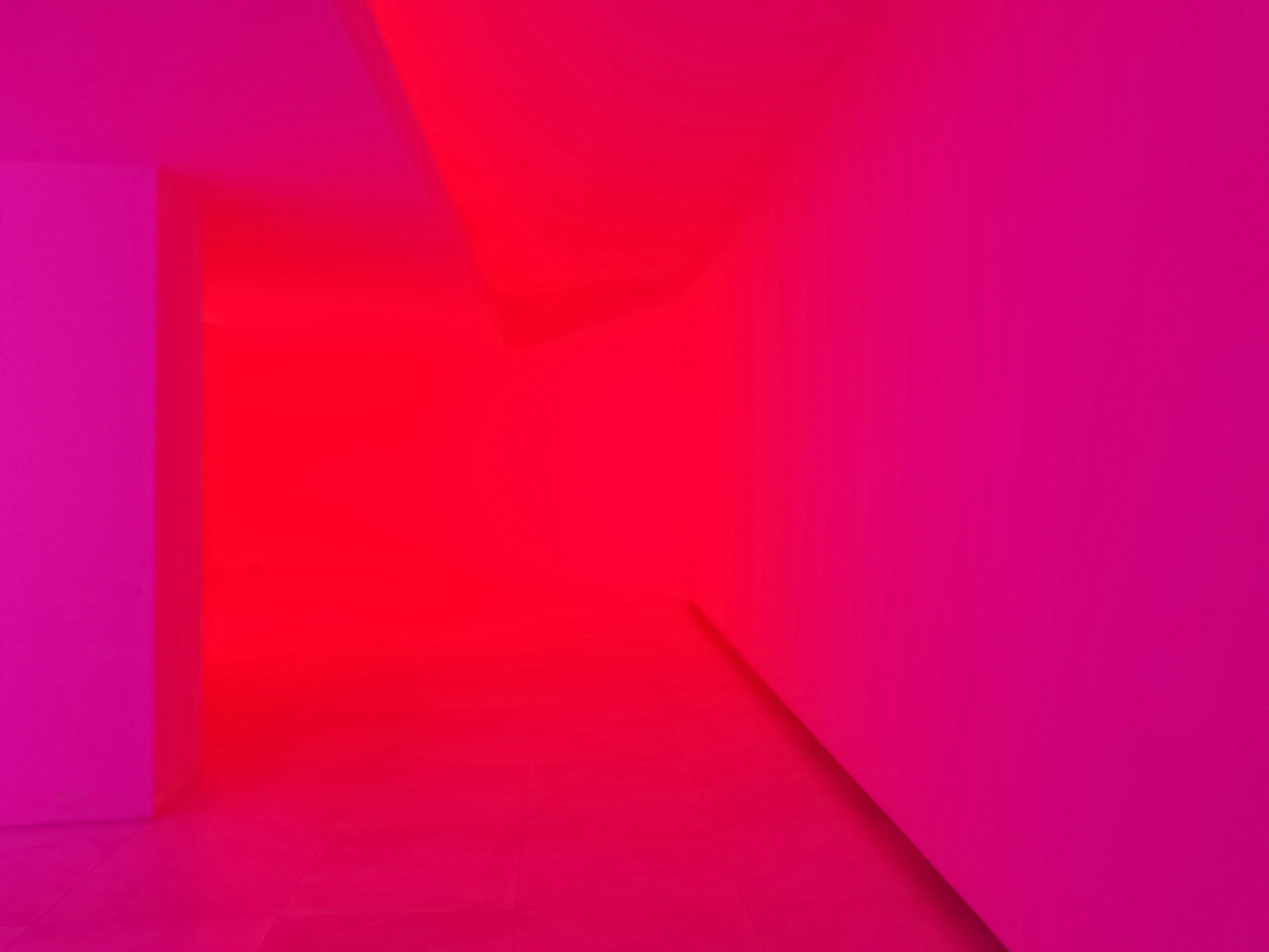 Abstract interior space illuminated with deep pink lighting, creating a surreal atmosphere. The geometric forms enhance the sense of depth and perspective.