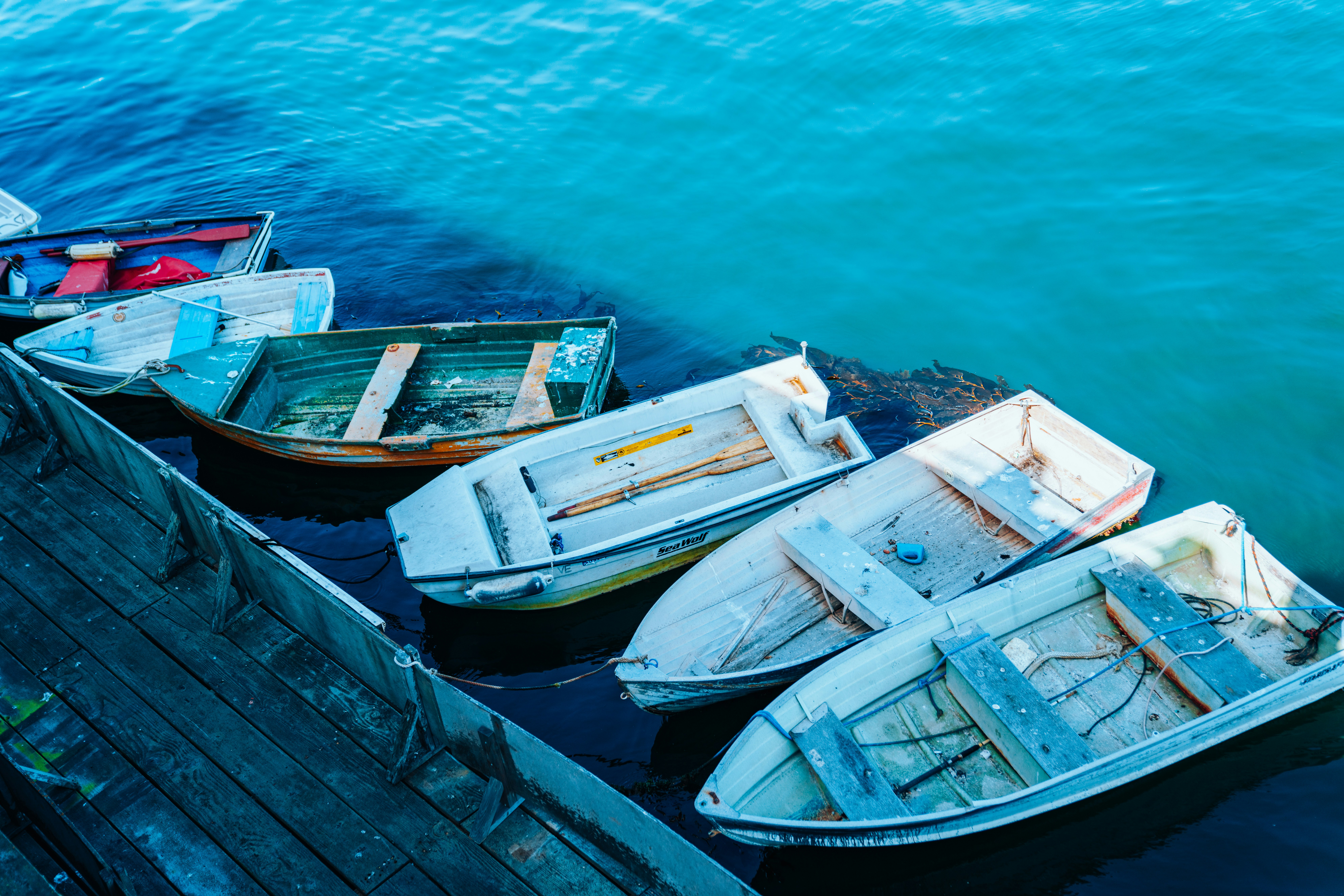 Weathered rowboats gently tethered beside a wooden dock on tranquil blue water.