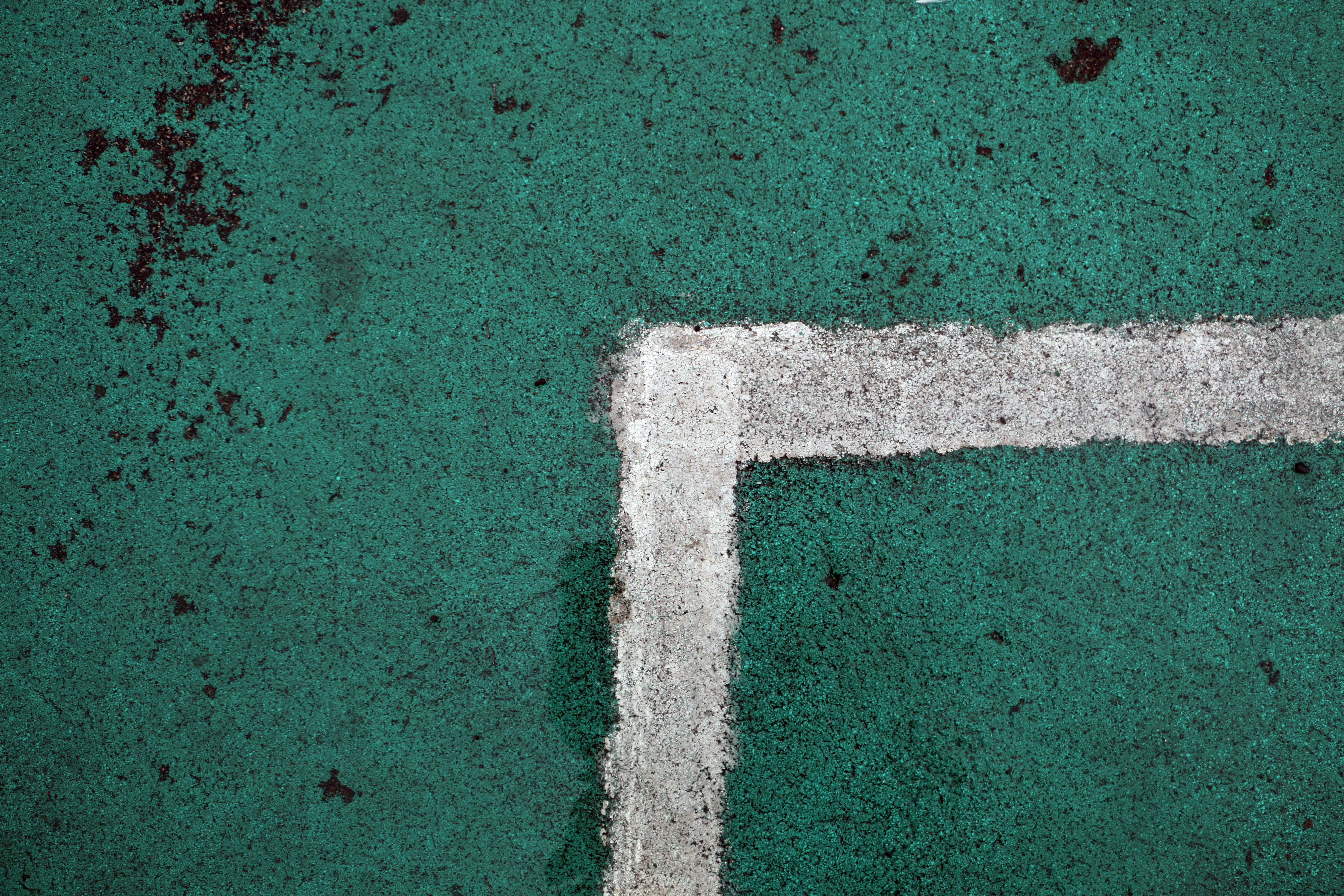 Worn white line on a textured green sports court, showcasing weathered surface details.