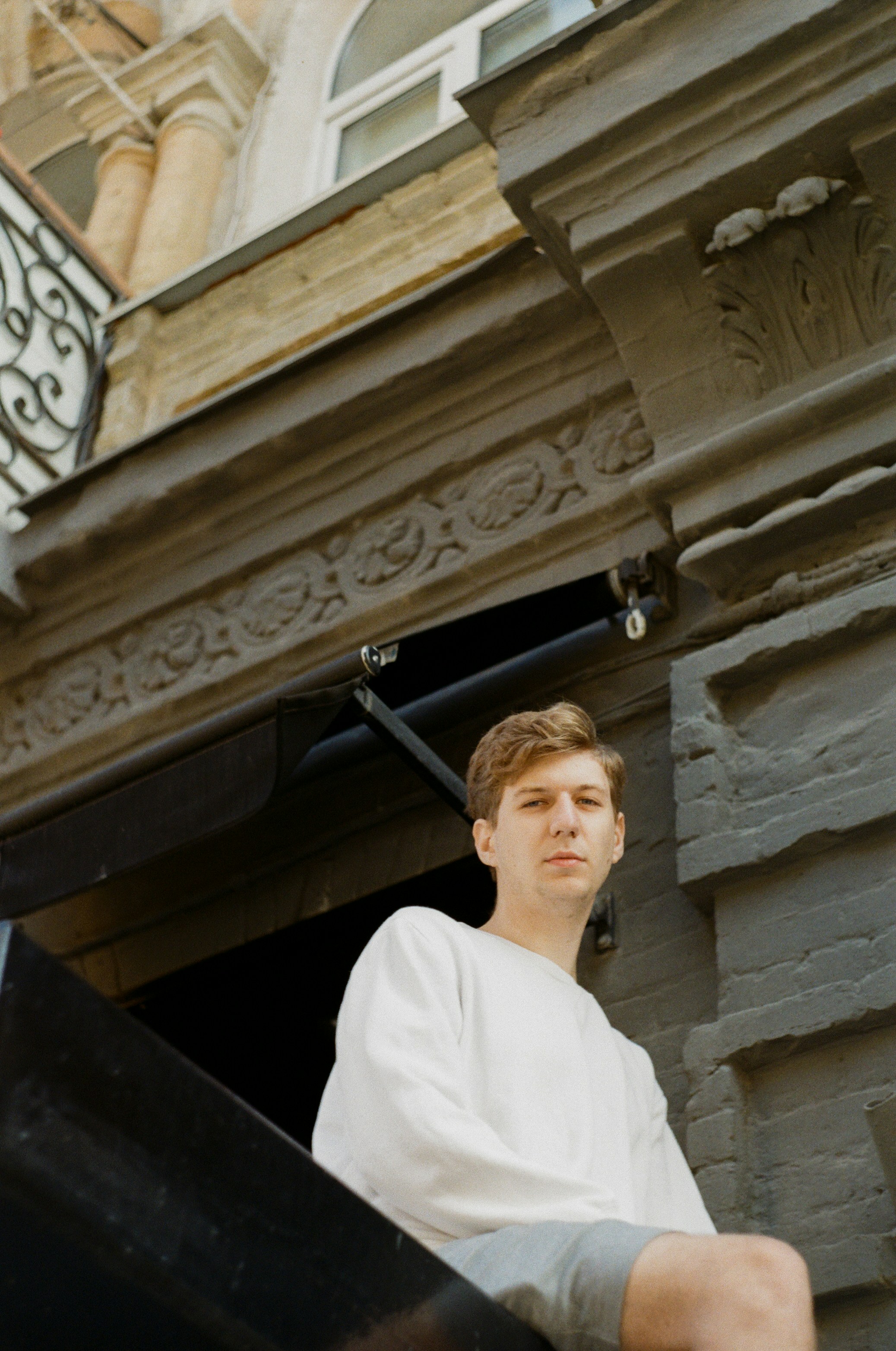 Young man seated on steps of a building, gazing contemplatively. The architectural details of the surroundings add depth to the scene.